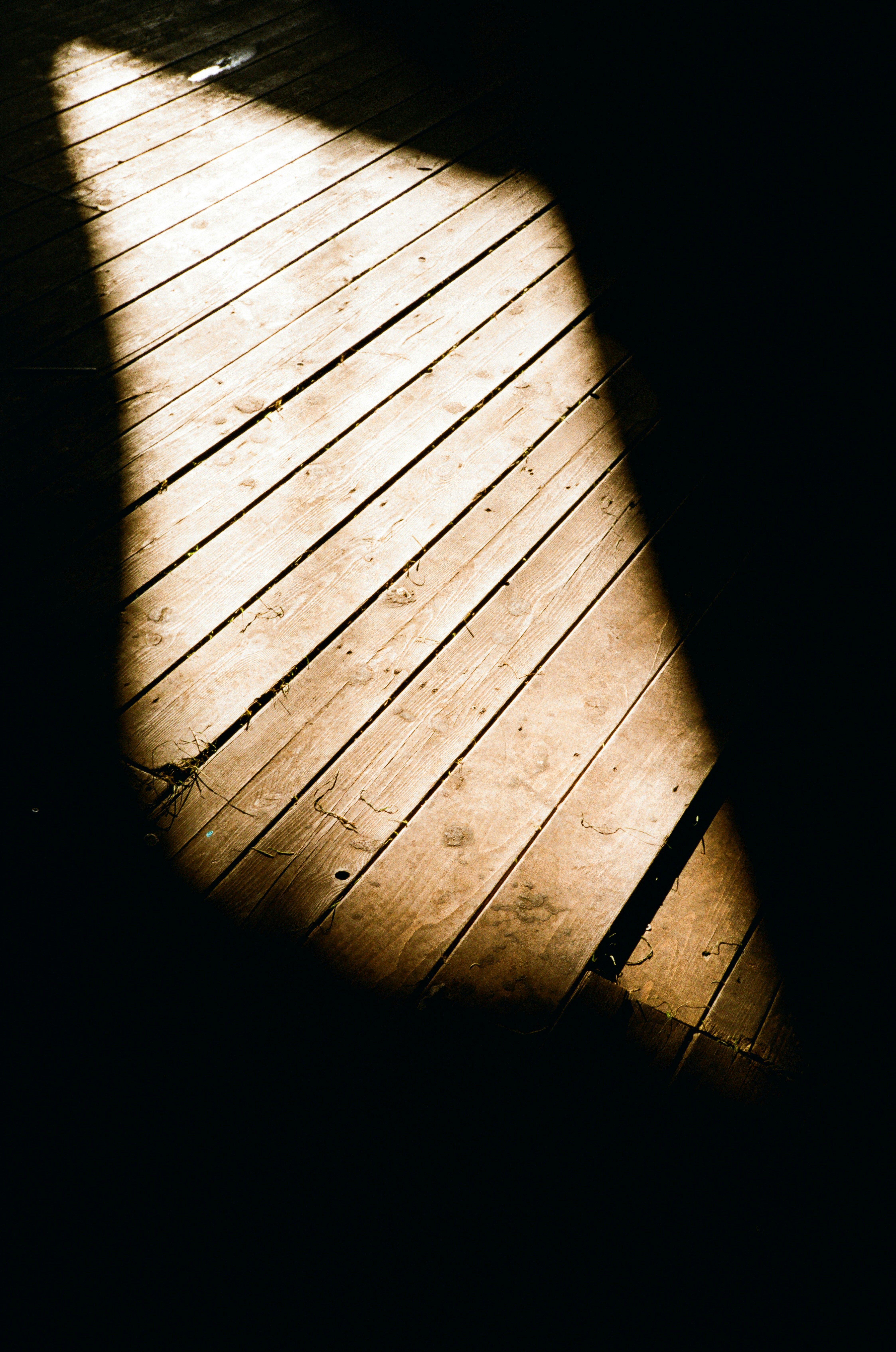 Sunlit wooden deck boards partially shaded, with a strong vignette framing the bright foreground; a minimal, moody composition highlighting texture and grain.