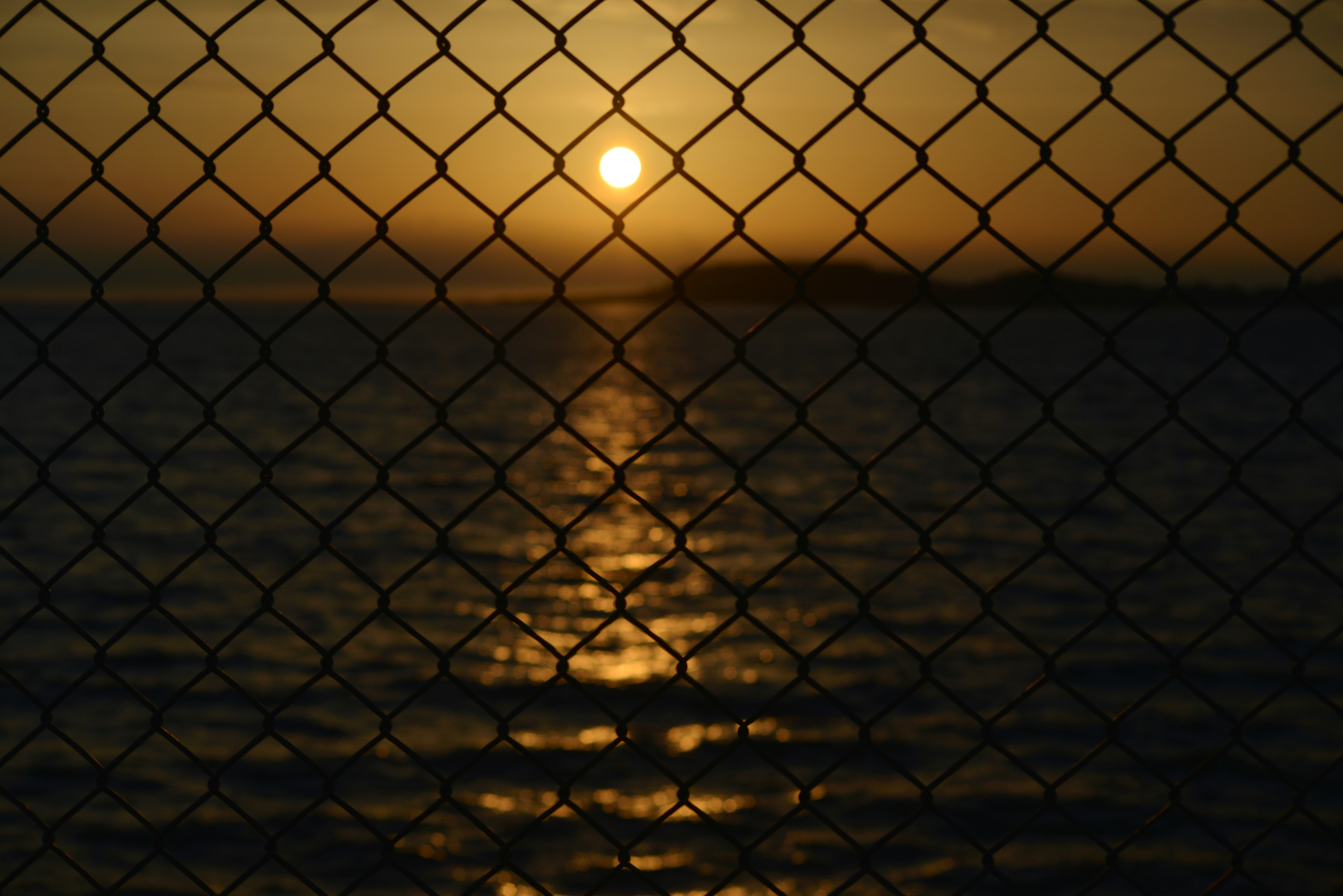 Sunlit Mesh: Sunset Through a Chain-Link Curtain over calm water