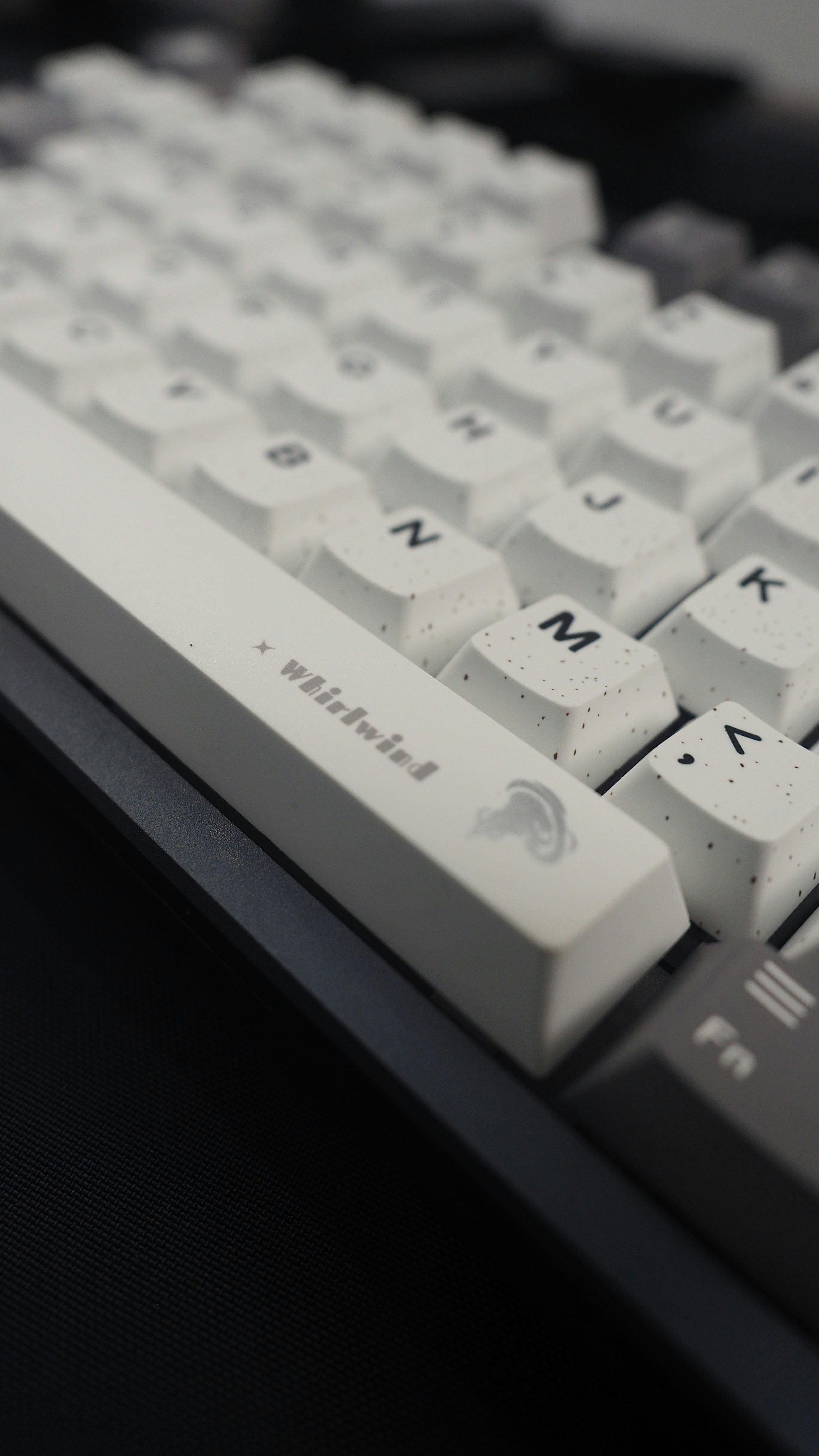 Close-up of a white mechanical keyboard with speckled keys and a Windwind logo, focused on the key row and surrounding texture.
