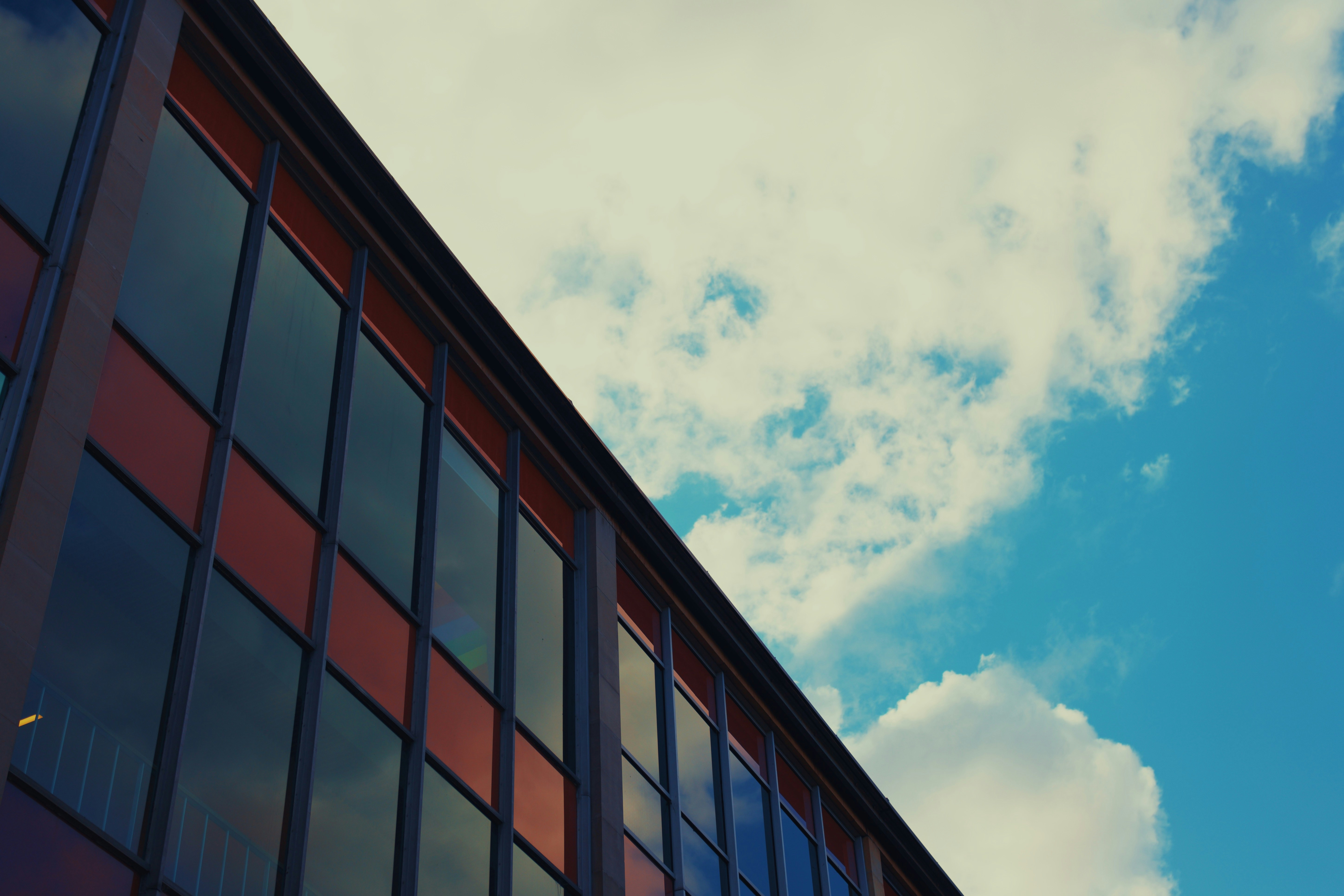 Modern glass building faces a vivid blue sky with scattered clouds, emphasizing reflective panels and bold color blocks.