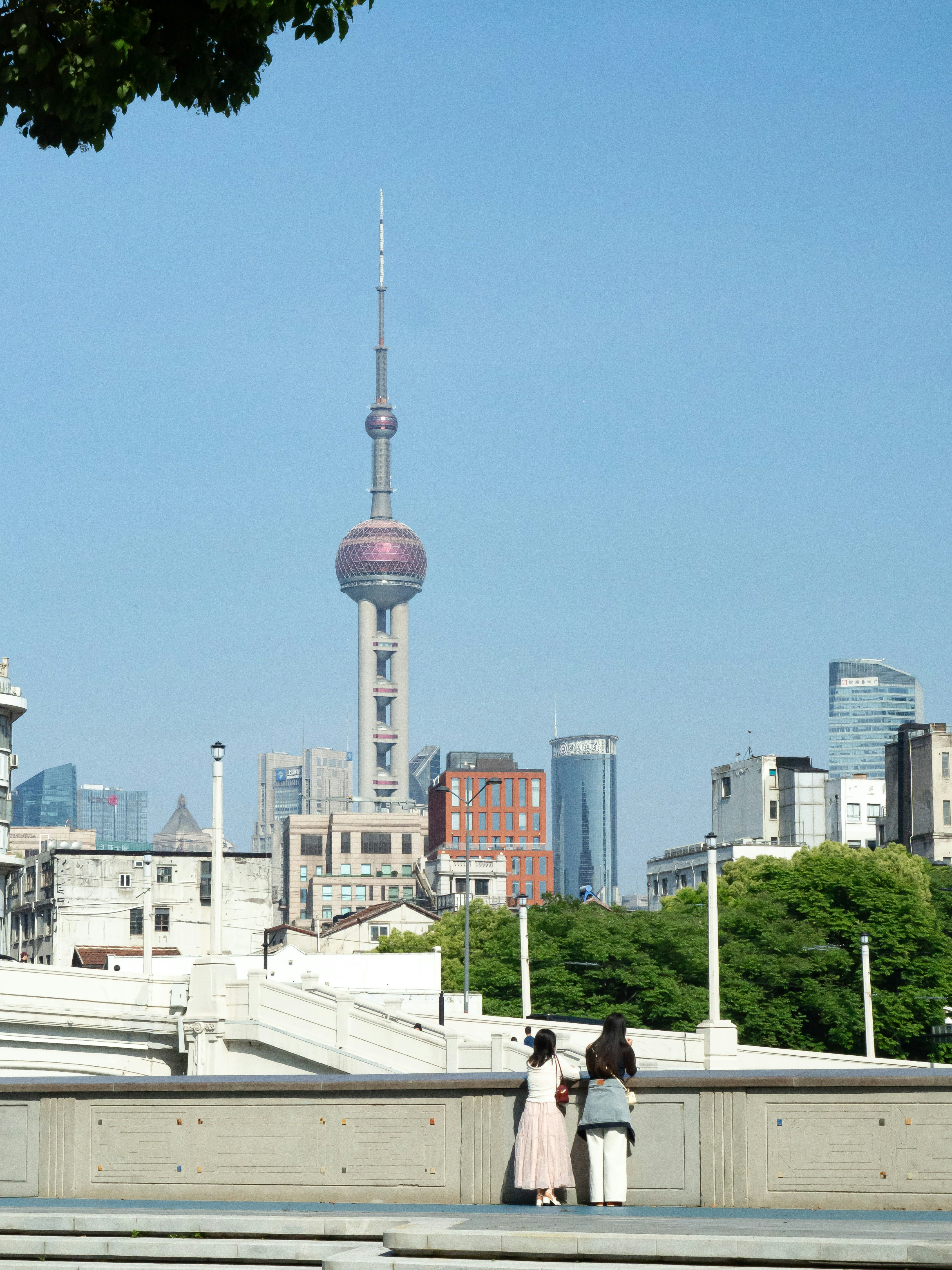 Two figures on a city bridge gaze toward a skyline dominated by a futuristic tower