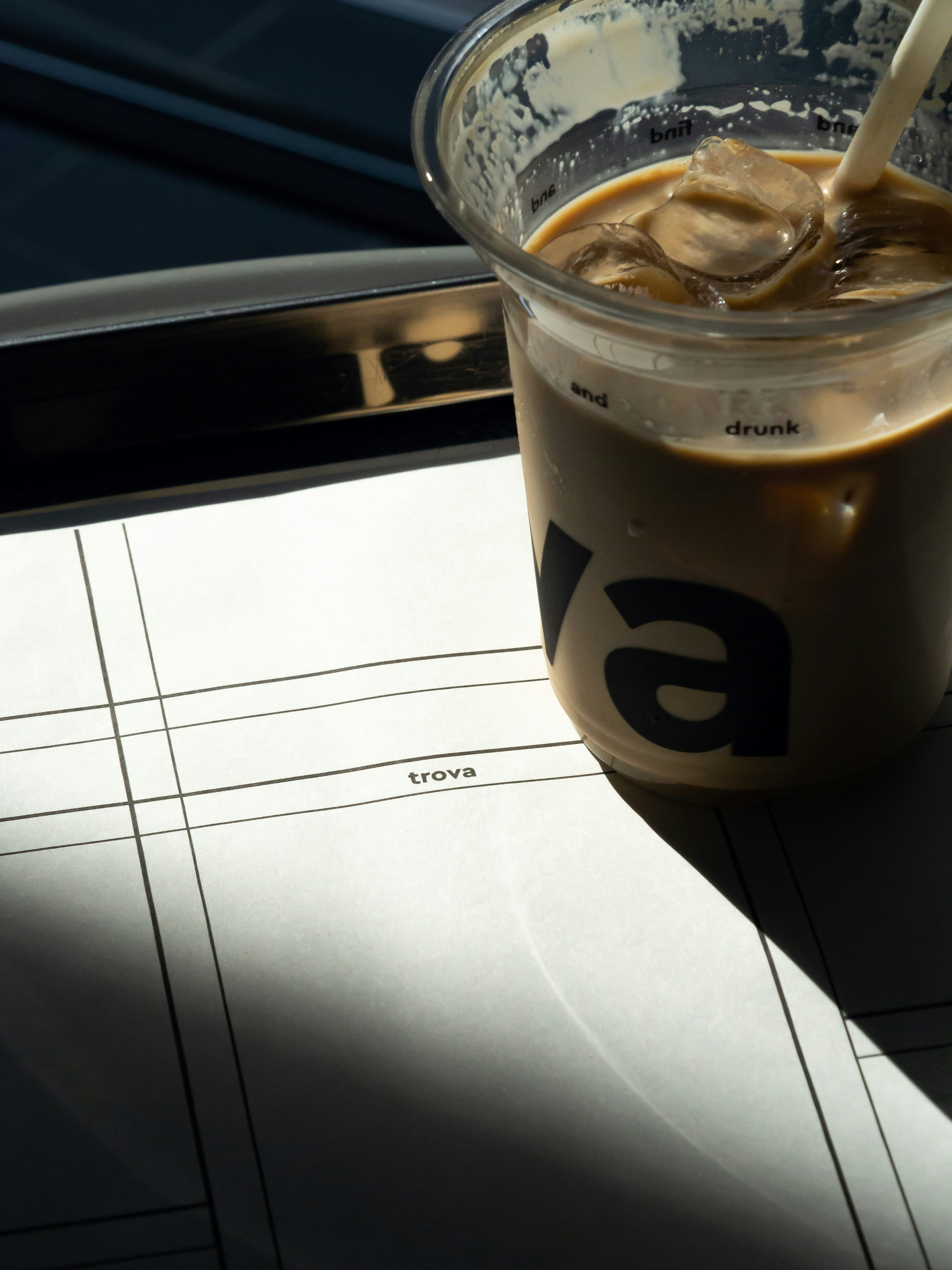 Iced coffee at a sunlit desk corner with printed lines