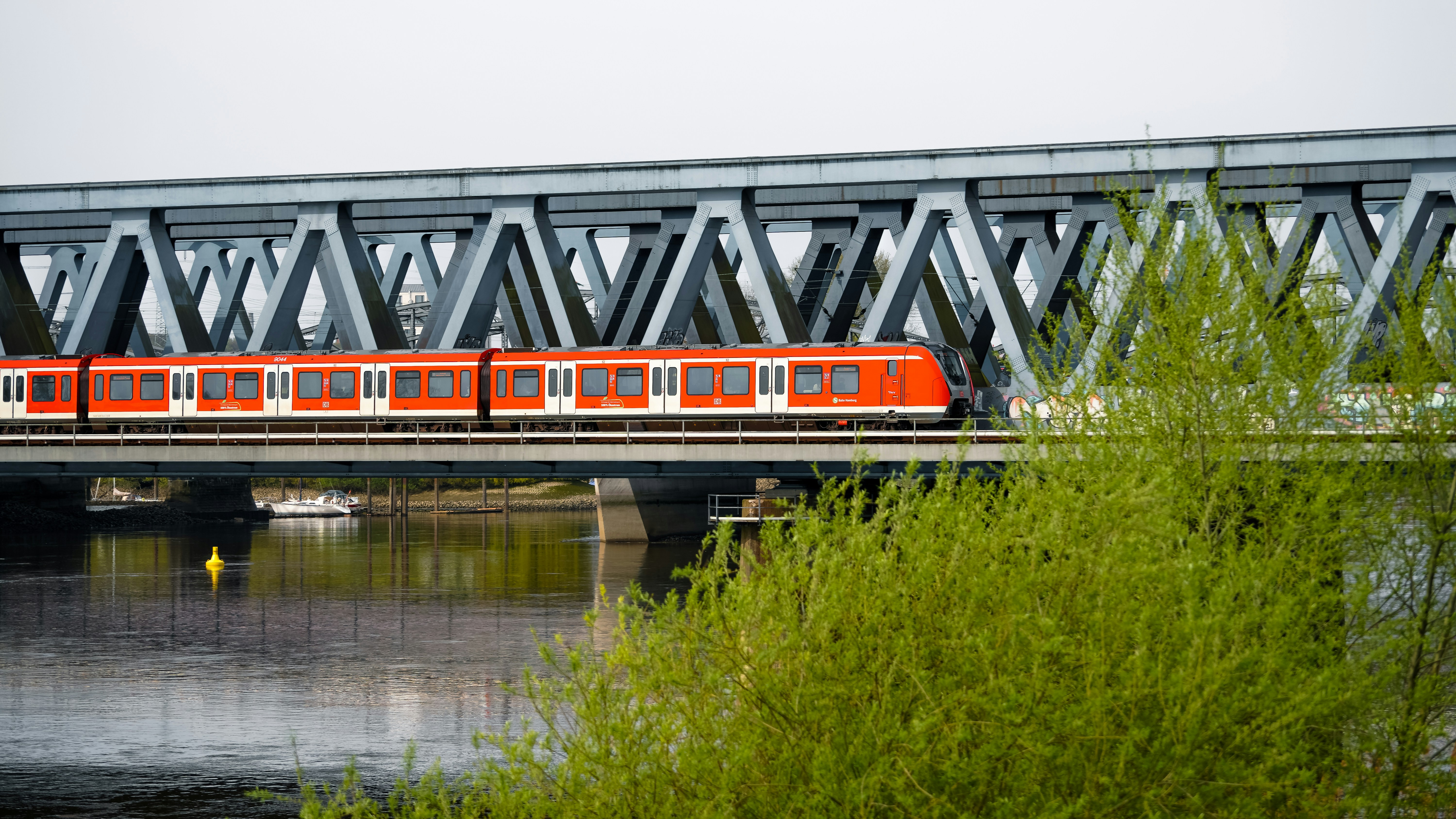 Orange commuter train crossing a steel truss bridge above a calm river