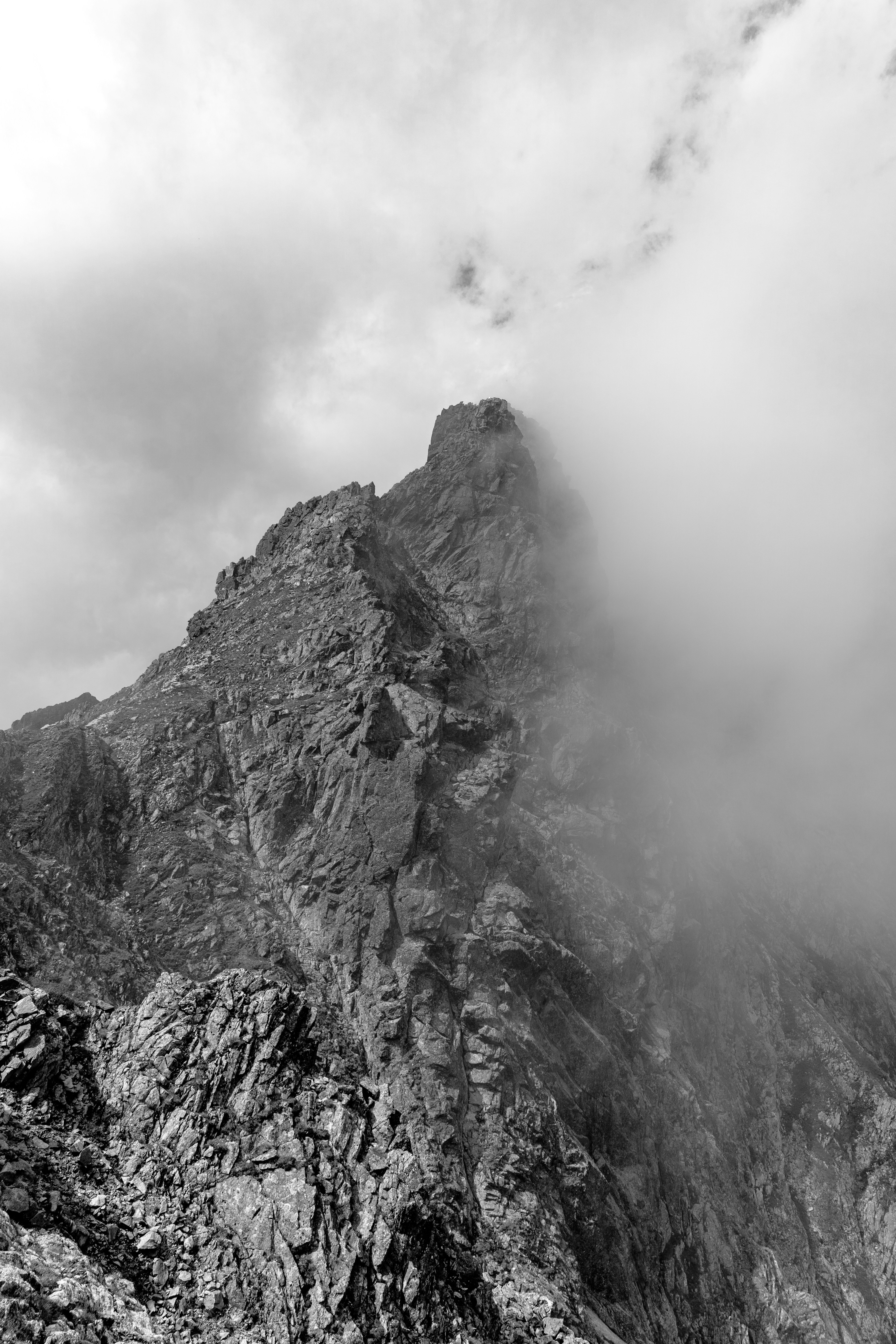 Serrated mountain peak rising through low clouds in monochrome, emphasizing rugged texture and atmospheric mood.