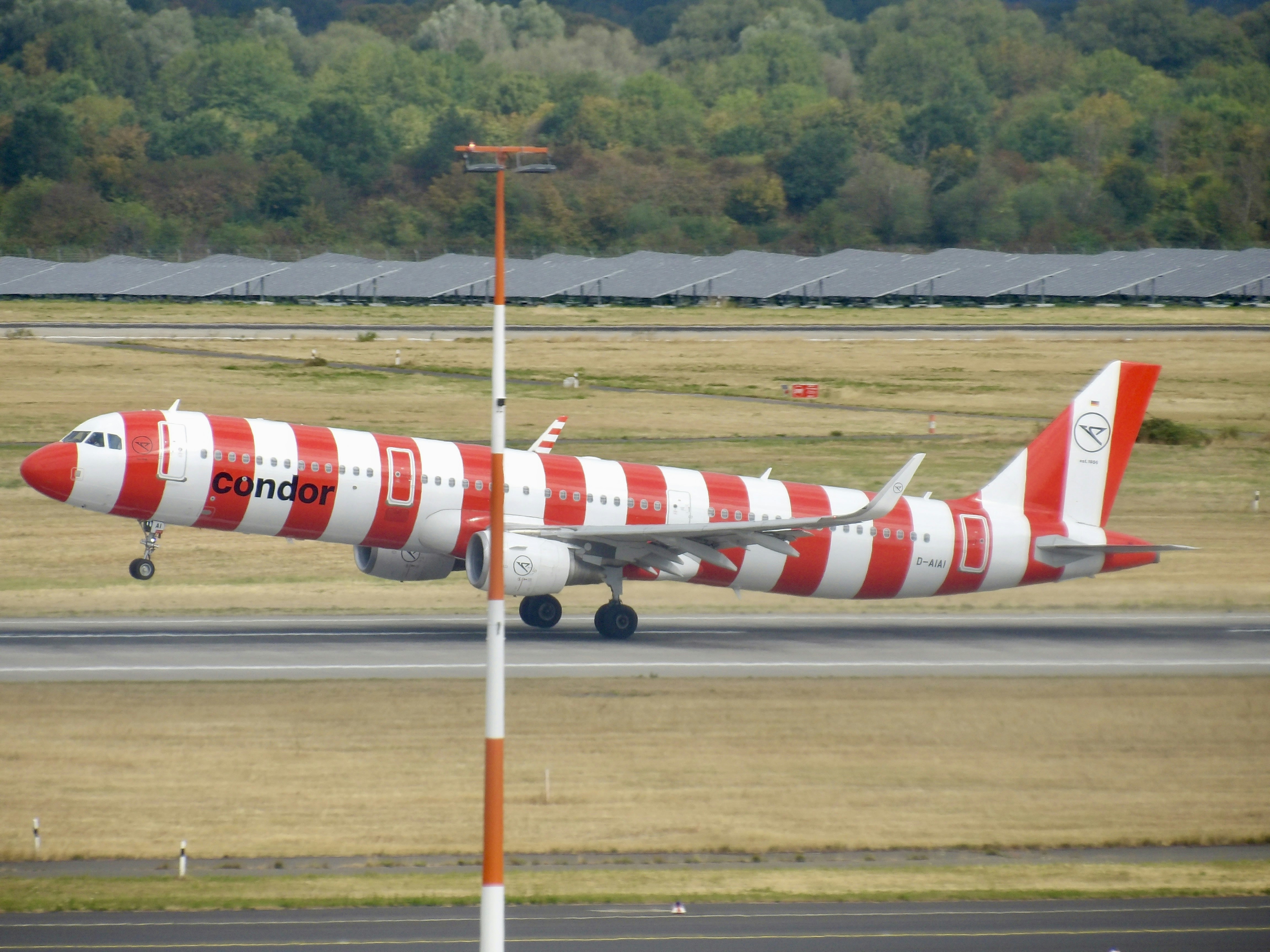 A striped red-and-white aircraft taxis along a runway with a grassy field and distant hangars in the background.