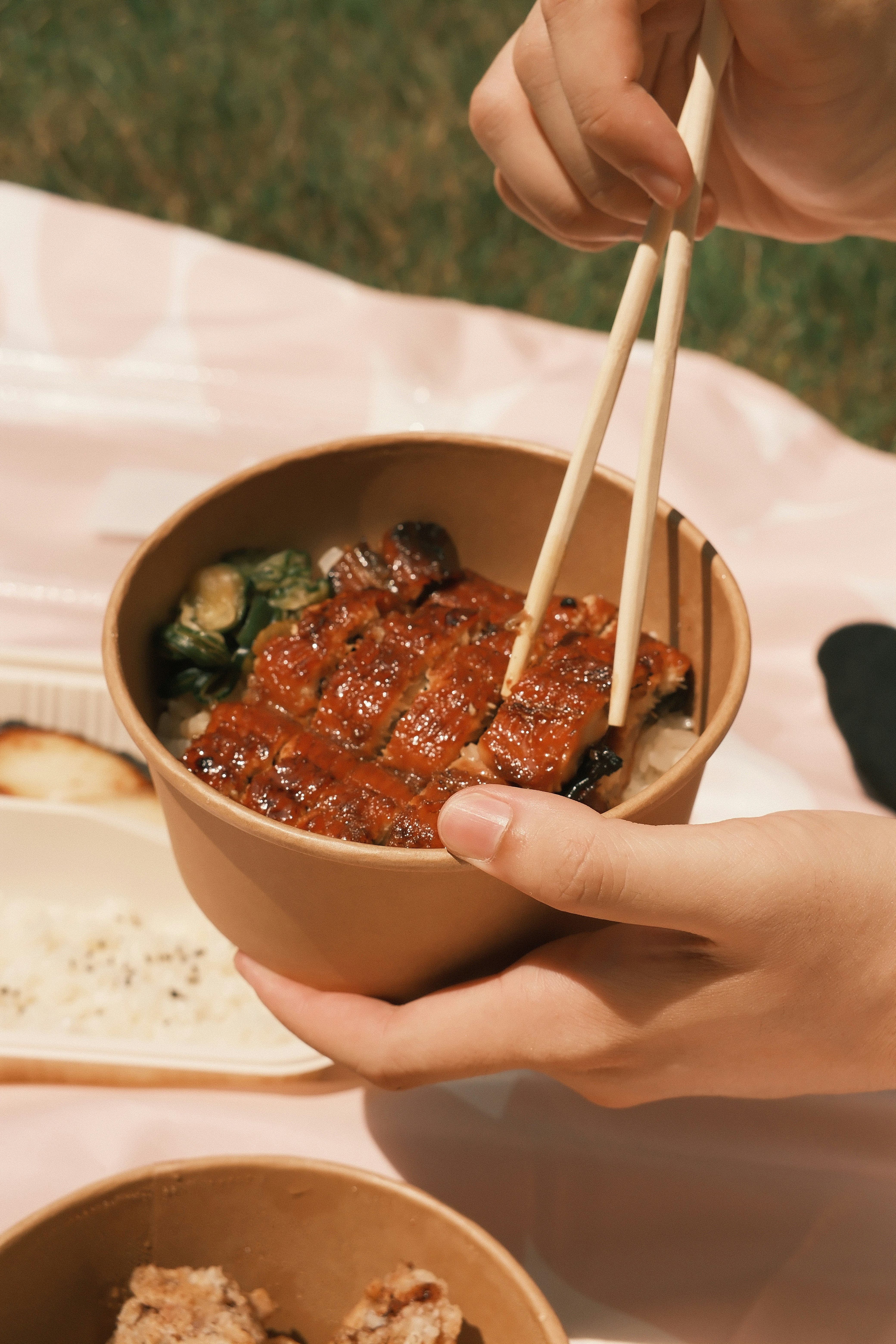 A person holding a bowl of grilled eel over rice with chopsticks