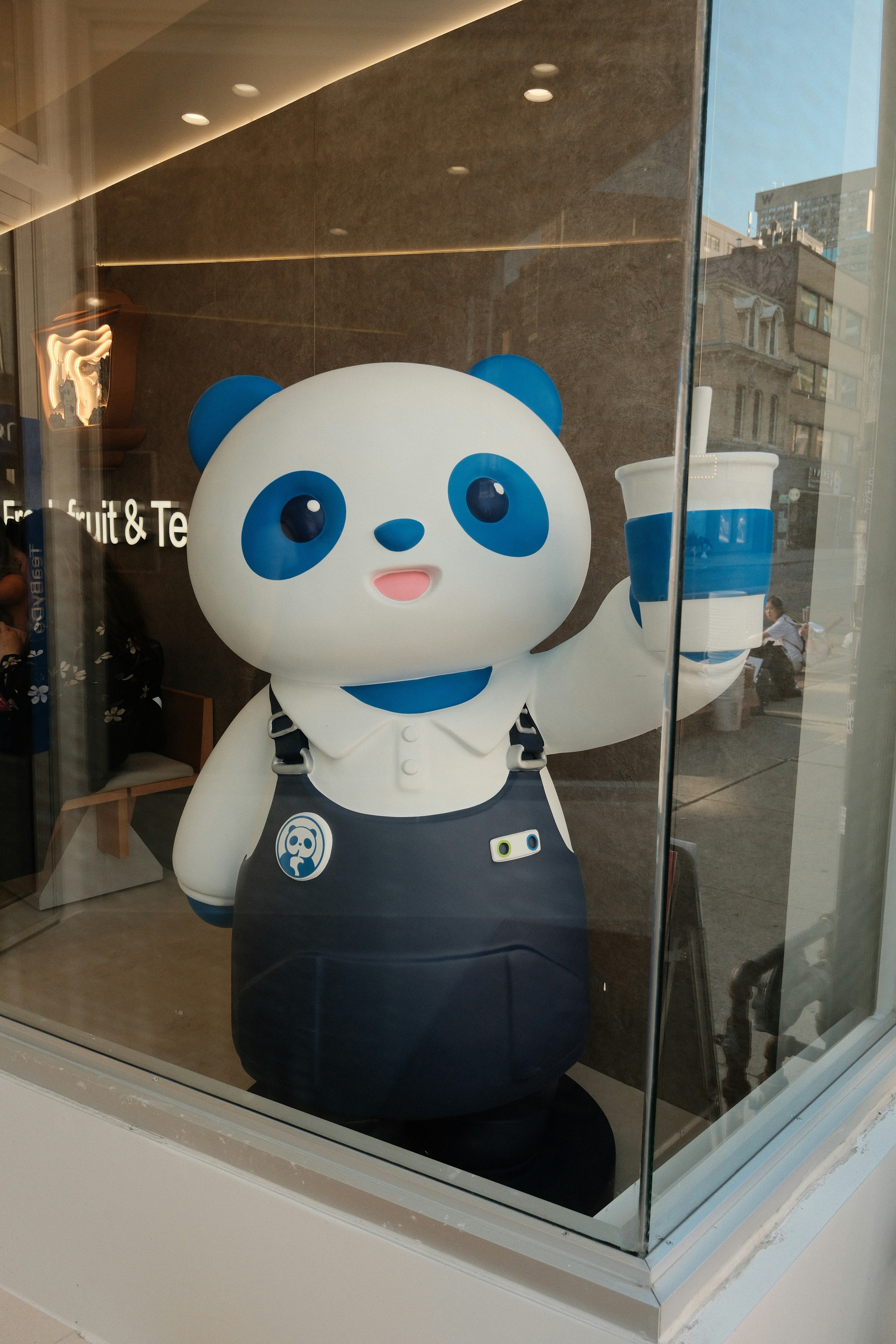 Panda mascot waves from a storefront window with a blue striped cup