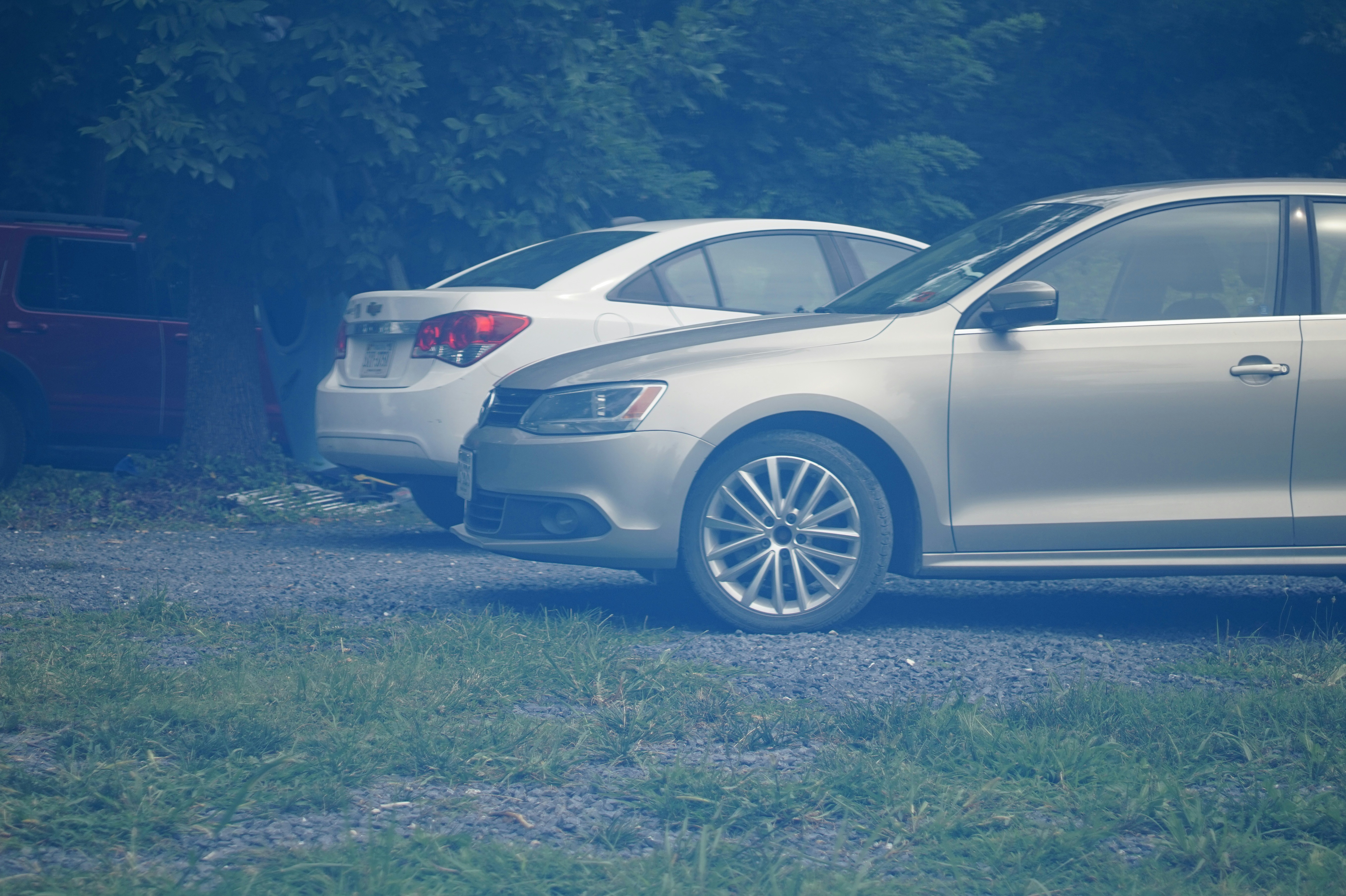 A silver sedan and a white sedan parked on a gravel lot