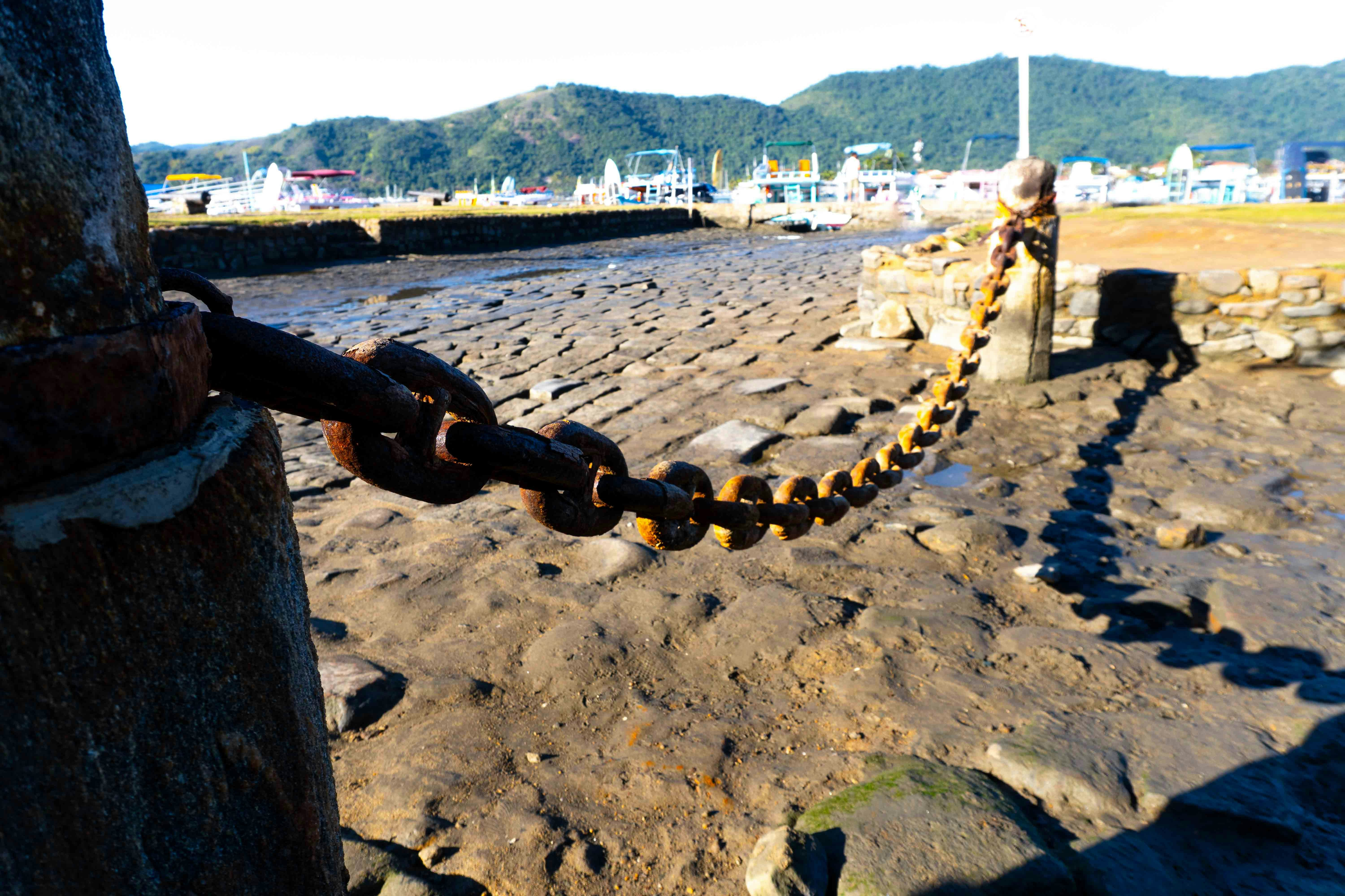 A heavy rusted chain connecting two stone bollards on a muddy tidal flat
