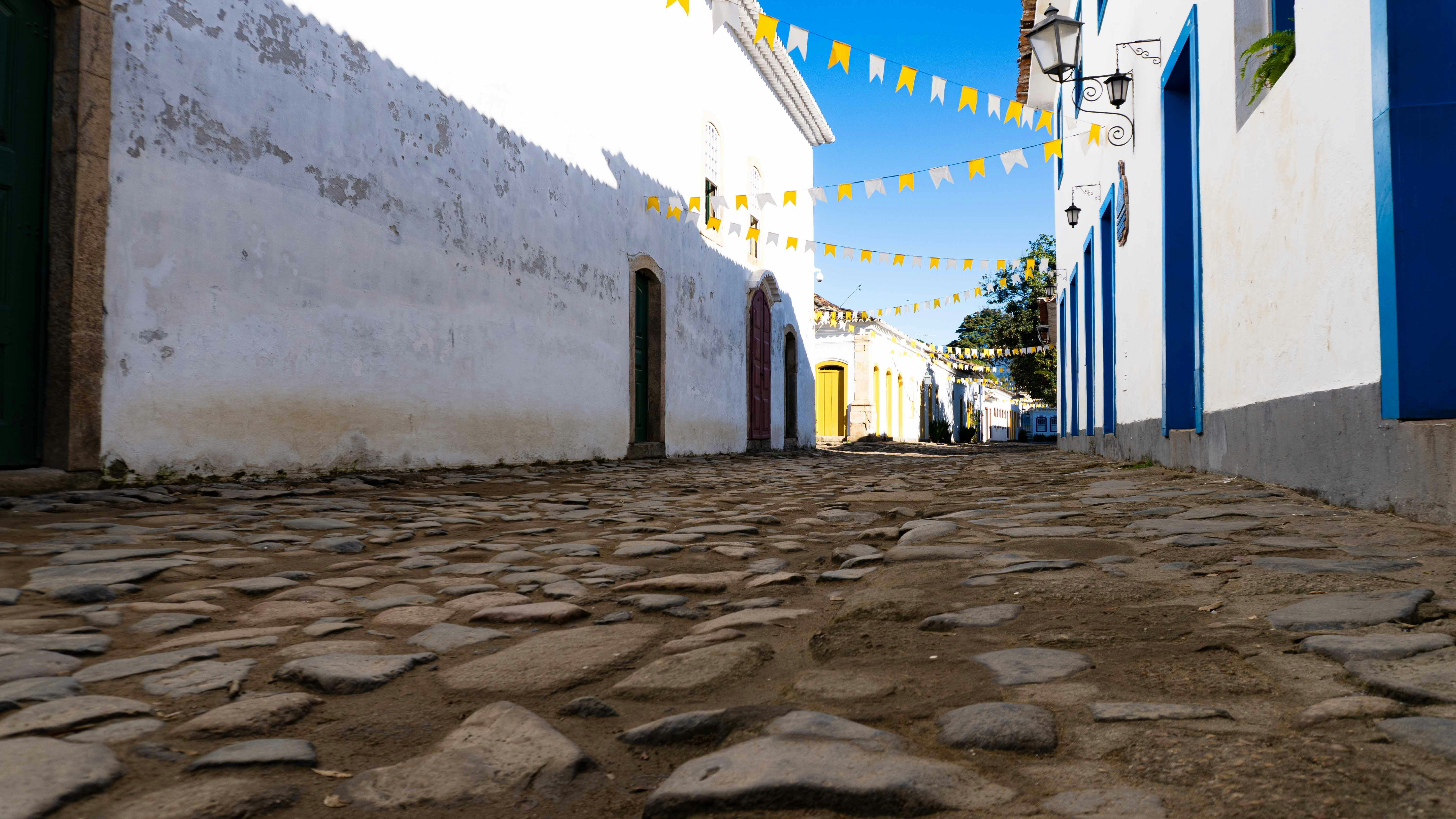 A cobblestone street between white buildings decorated with yellow pennant flags in Paraty