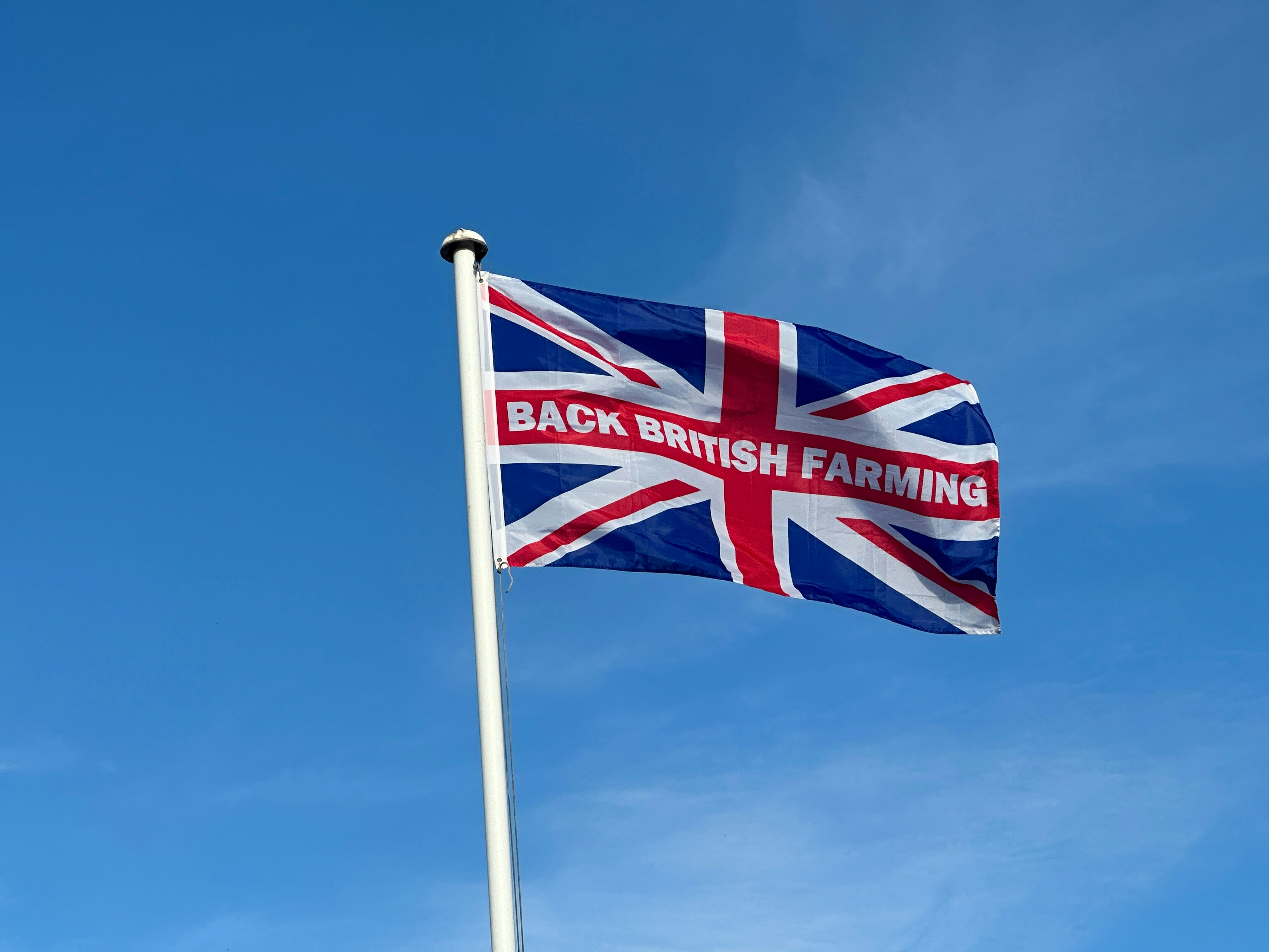 Union flag with ‘Back British Farming’, flying from flag pole against blue sky