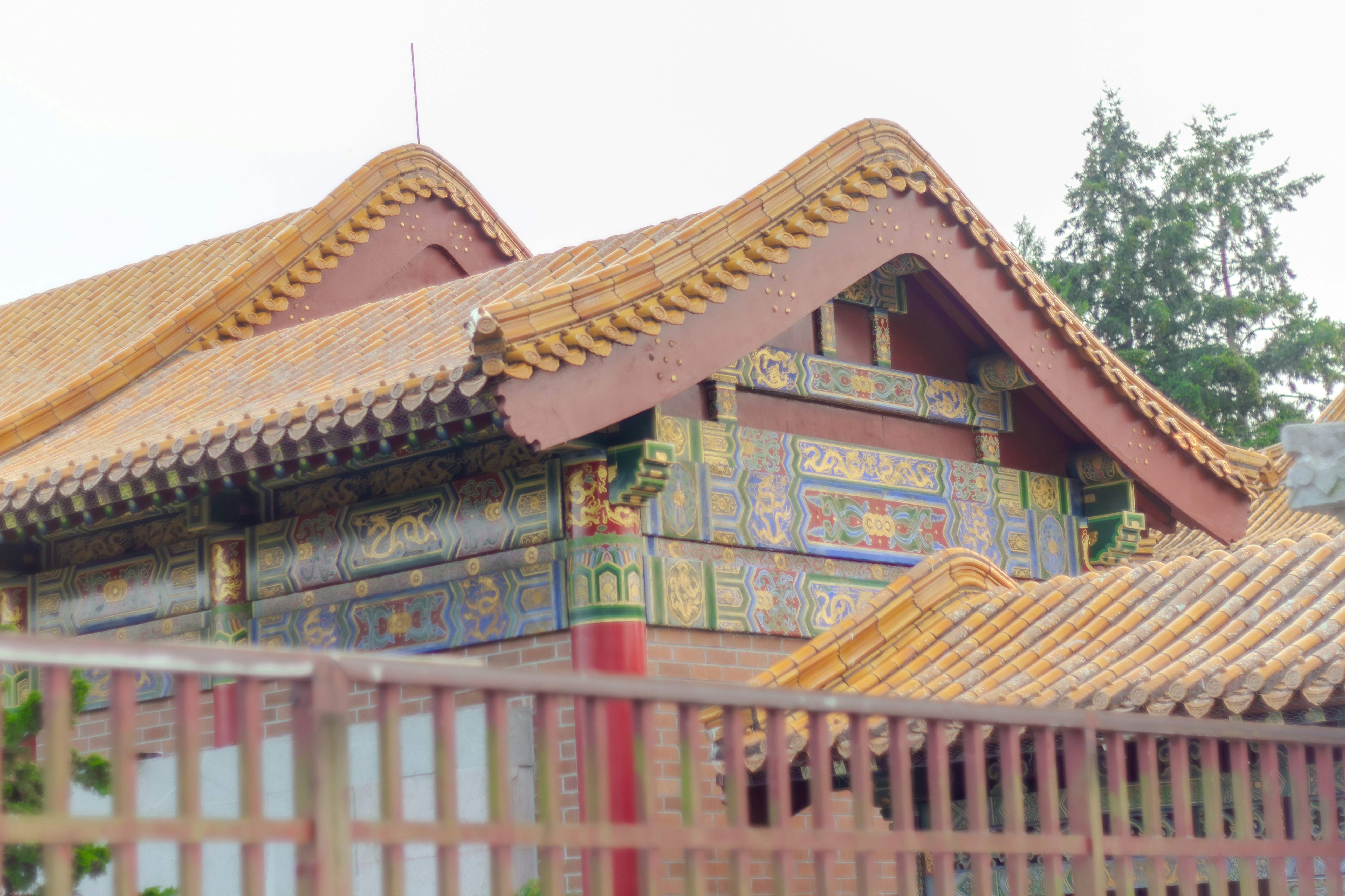 Colorful temple eaves and decorative beams framed by a rusty tiled roof and foreground railing.