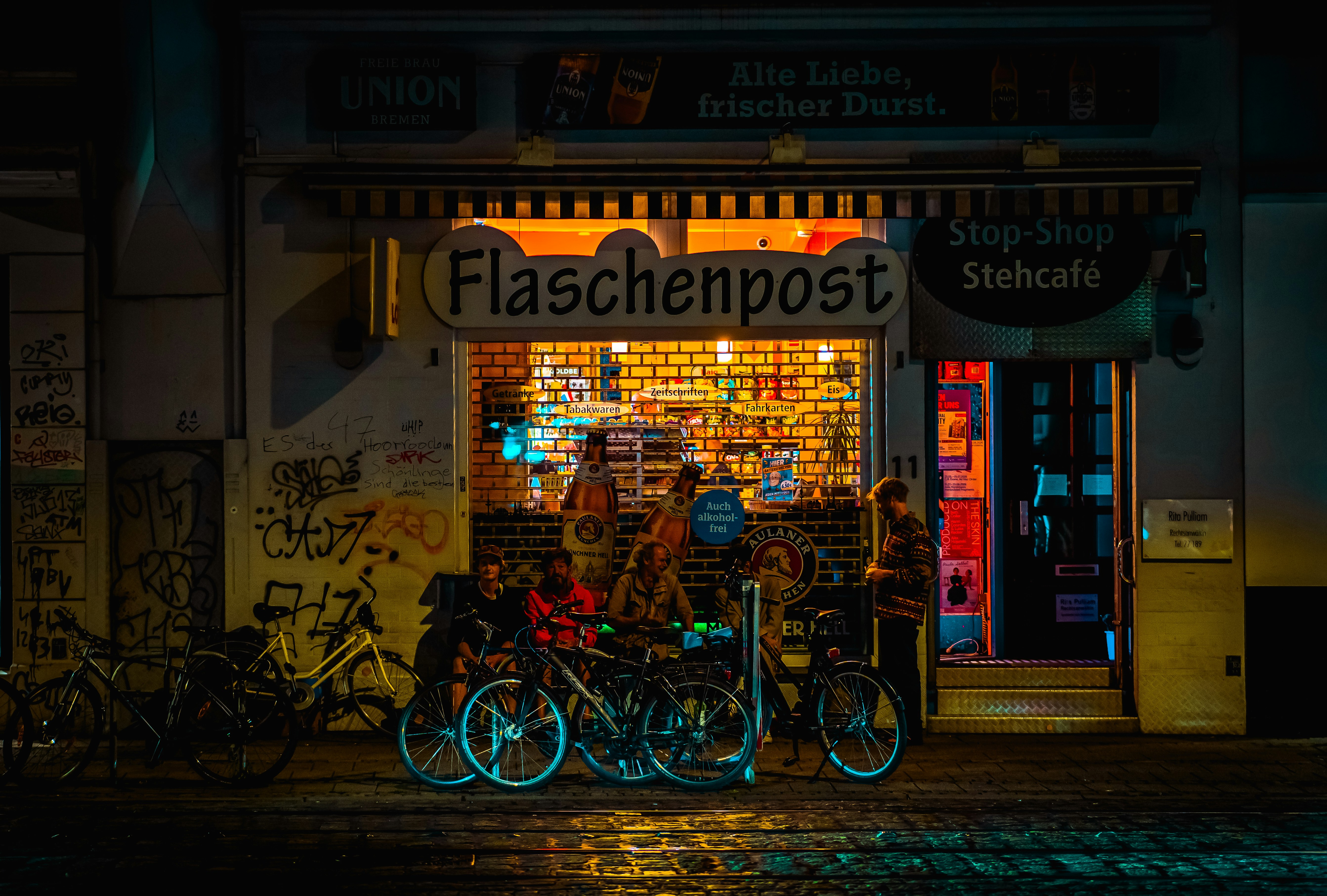 Neon-lit storefront with bicycles and silhouettes at night