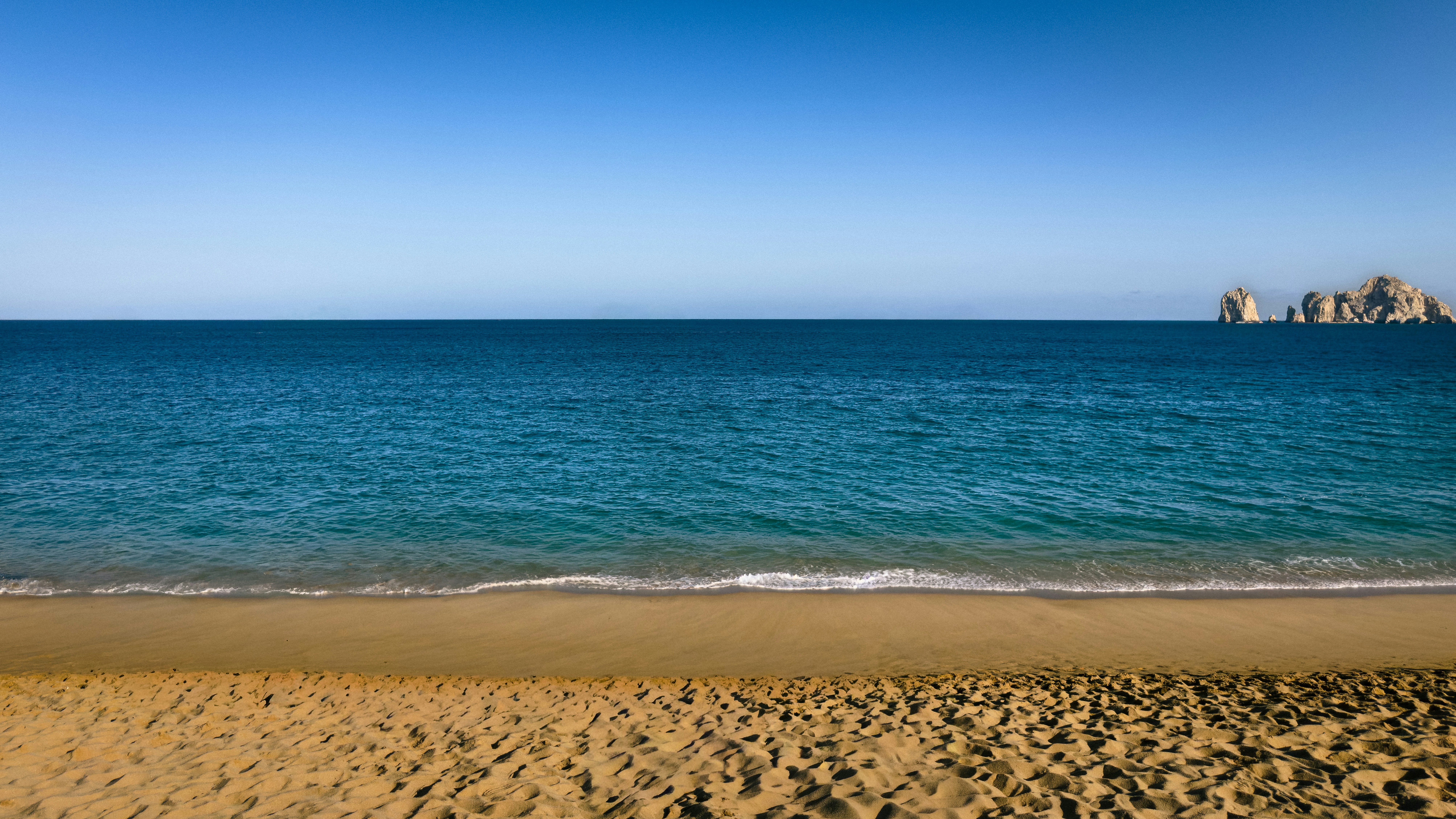 Golden beach with gentle waves meeting the shoreline under a clear blue sky; a calm seascape captured at the coast.