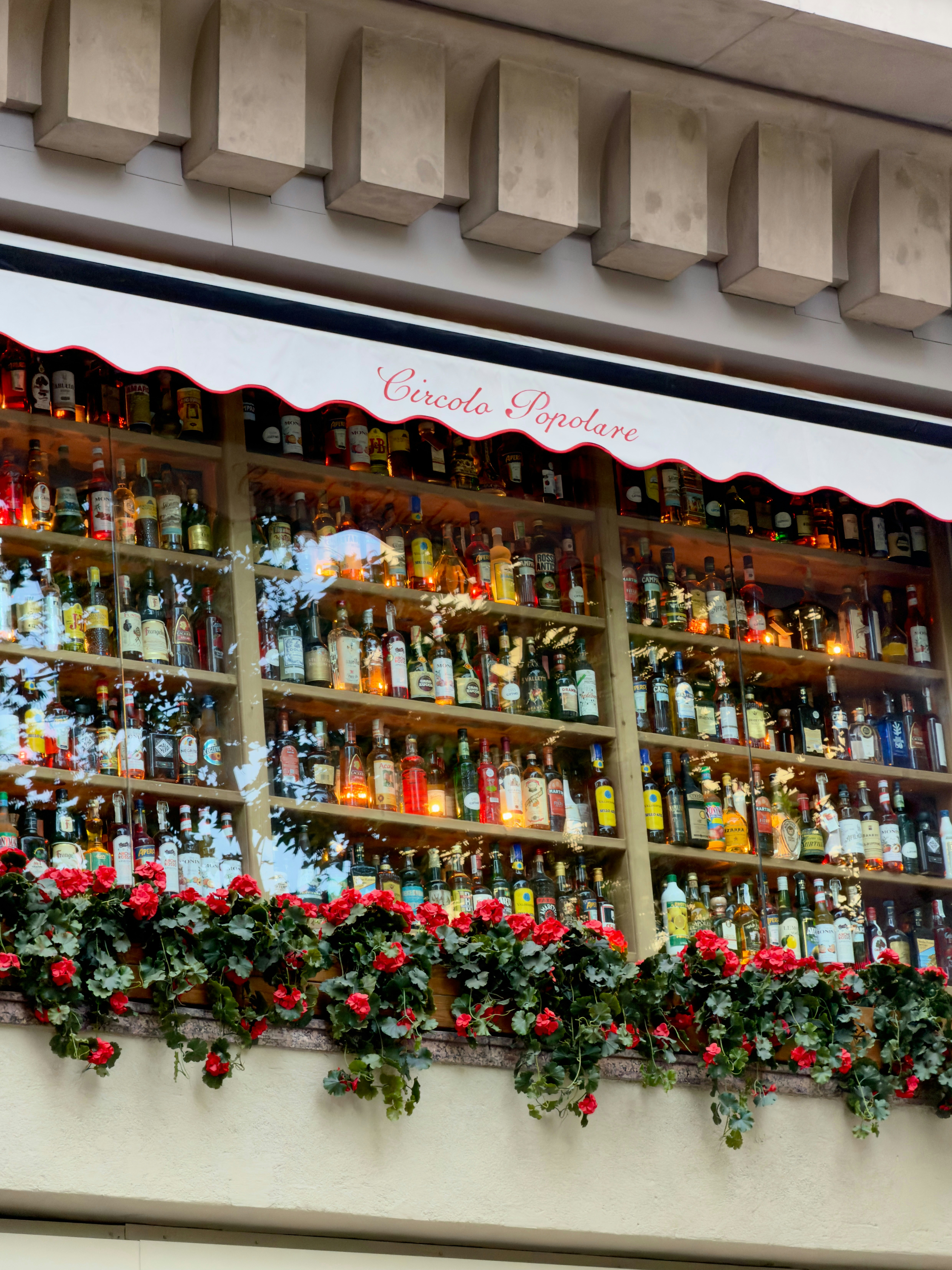 Glass-fronted Apothecary: Rows of Bottles Beneath Red Flowered Window Box