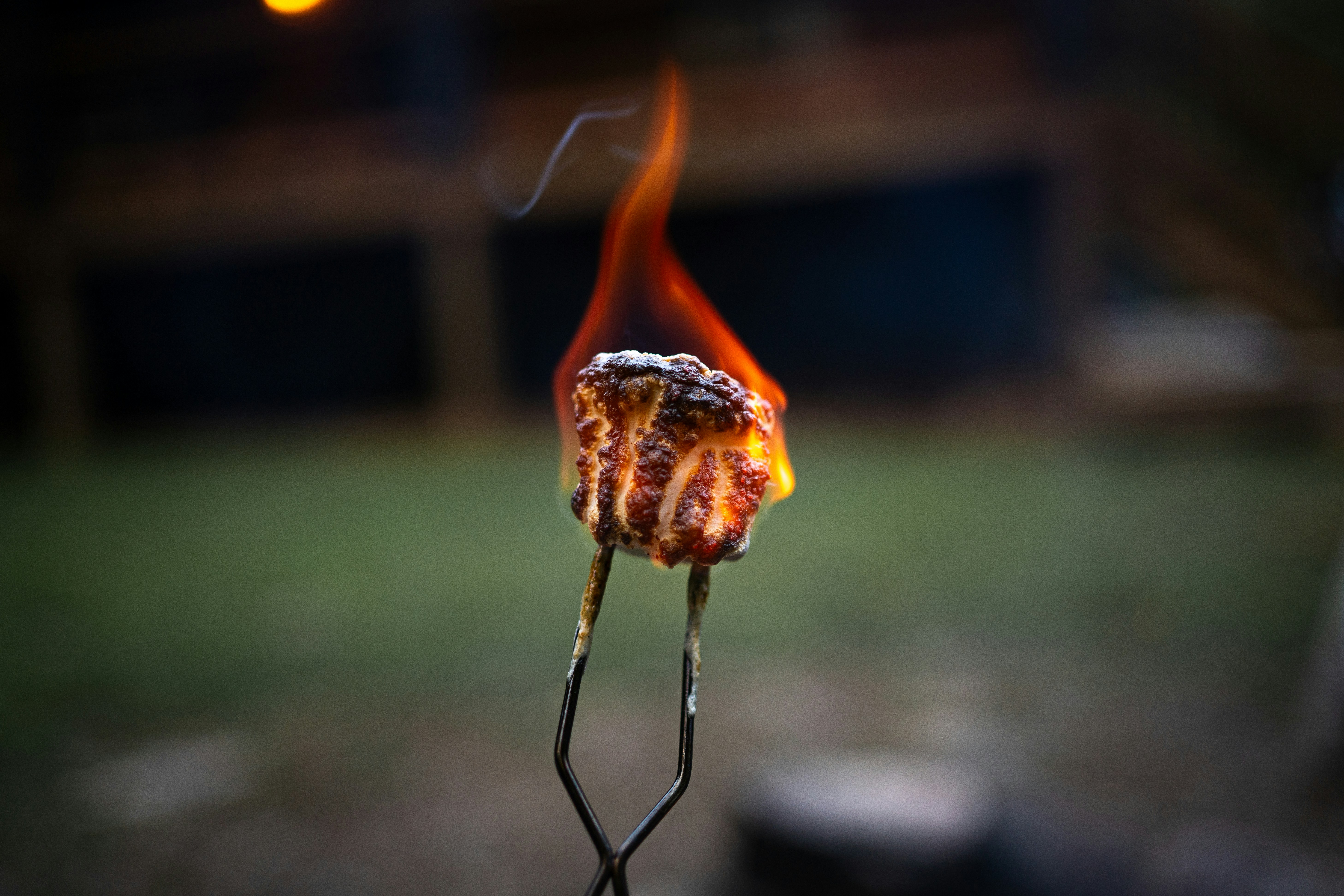 A single burning ember atop a bent metal pin stands out against a soft, defocused background, highlighting a small campfire moment.