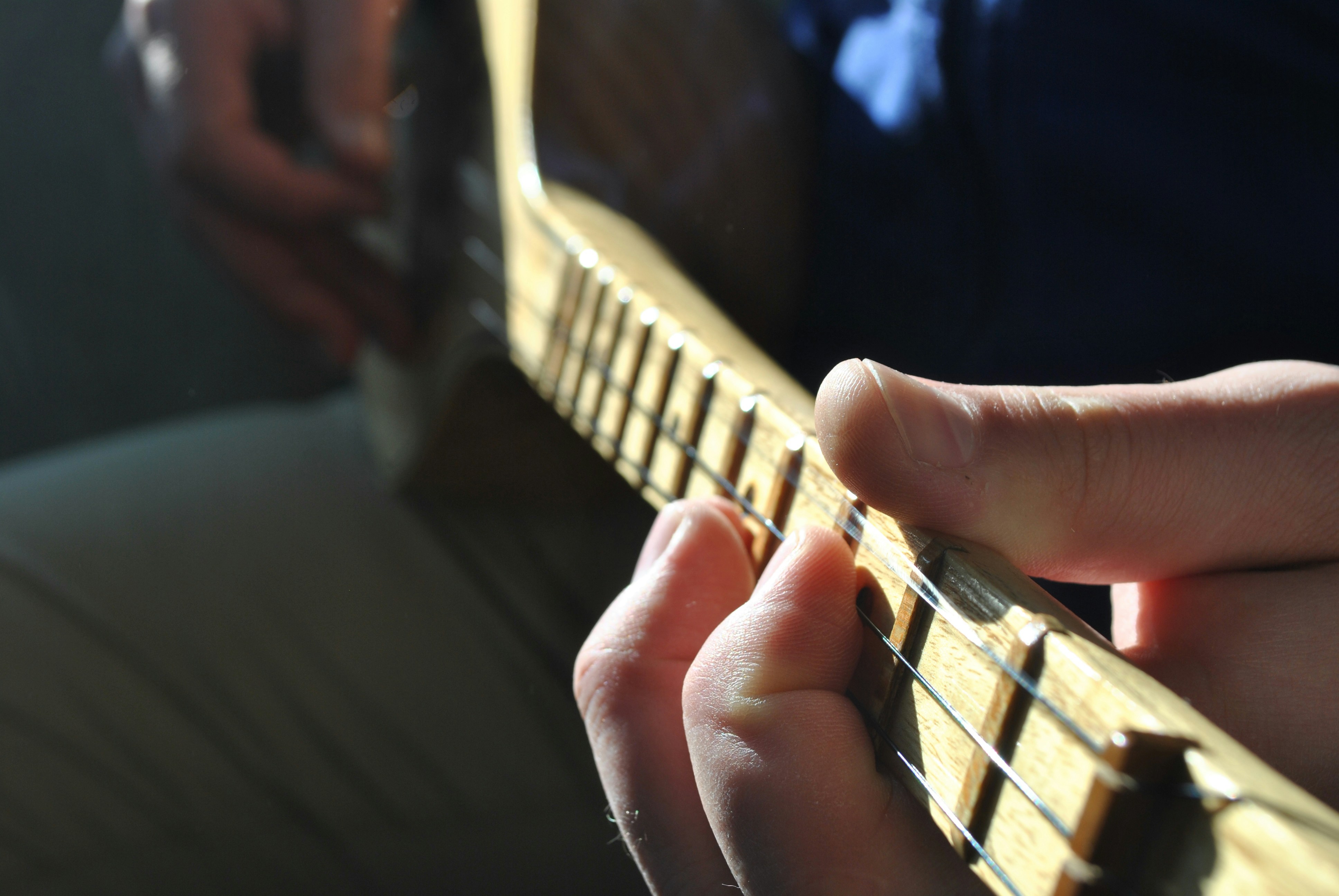 Close-up of fingers pressing guitar strings along the neck, focusing on the fretboard and hand positioning.