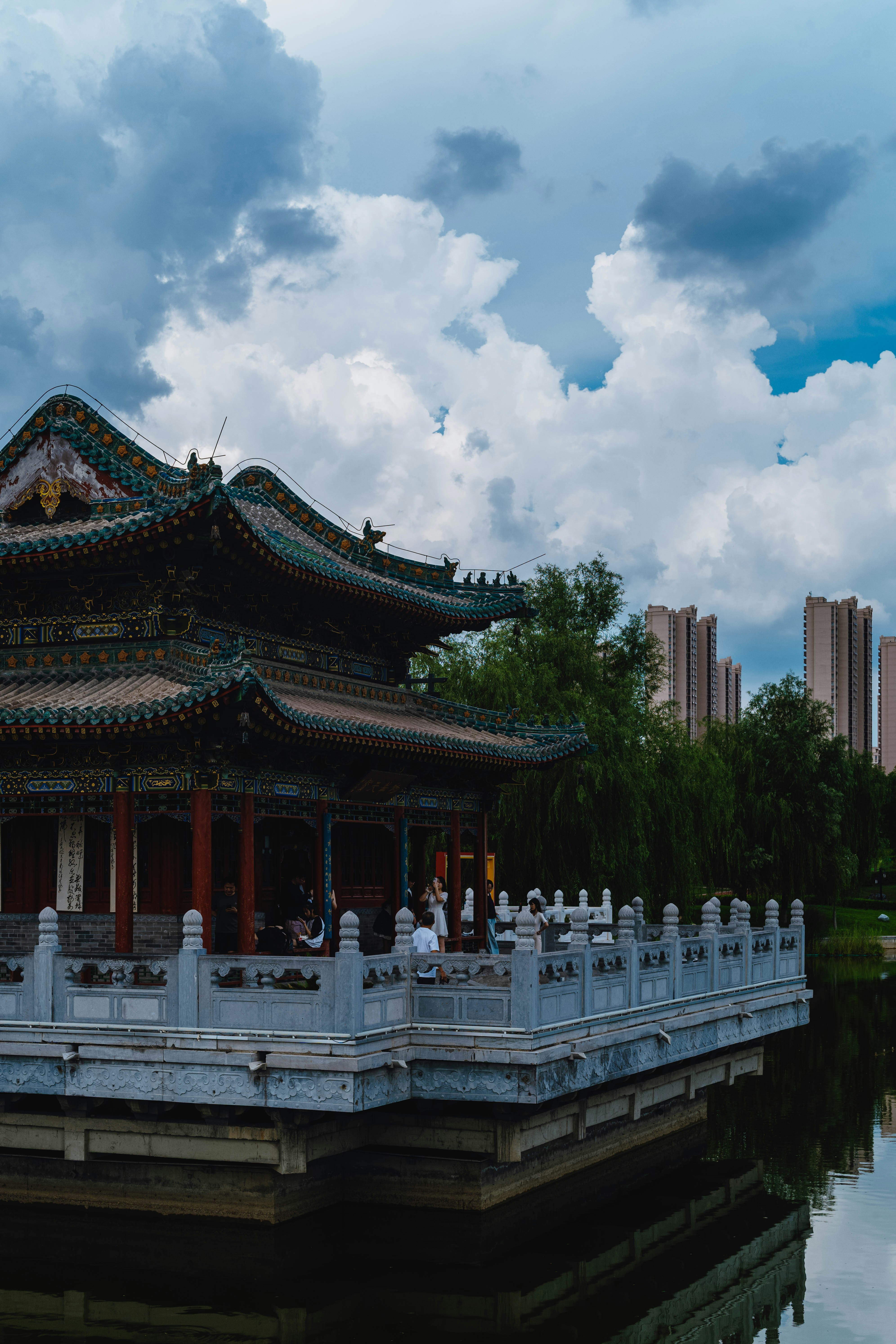 Traditional Pavilion Over Calm Pond Framed by Urban Silhouettes