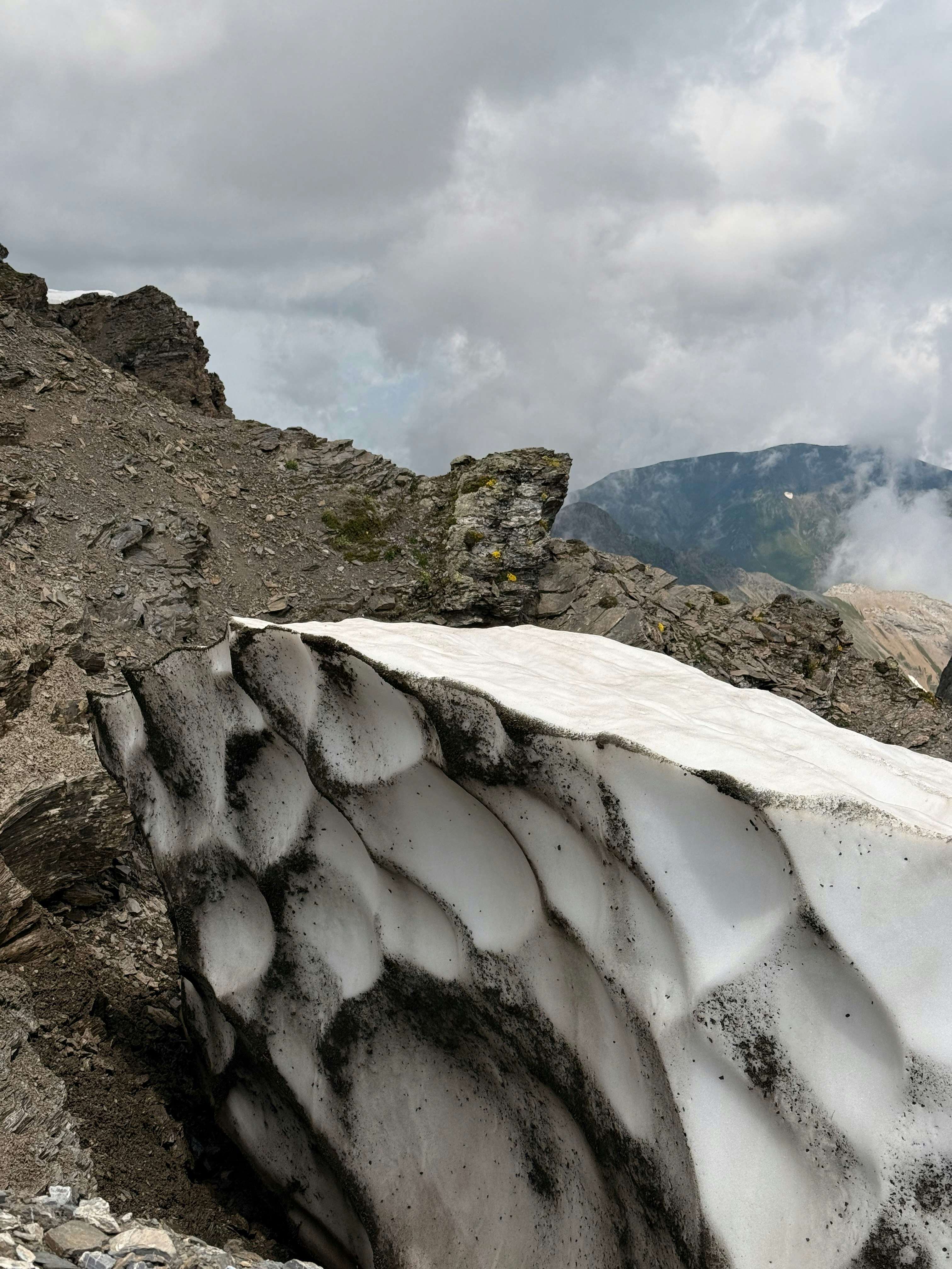 A glacier cleft tucked among jagged alpine rocks under a brooding sky