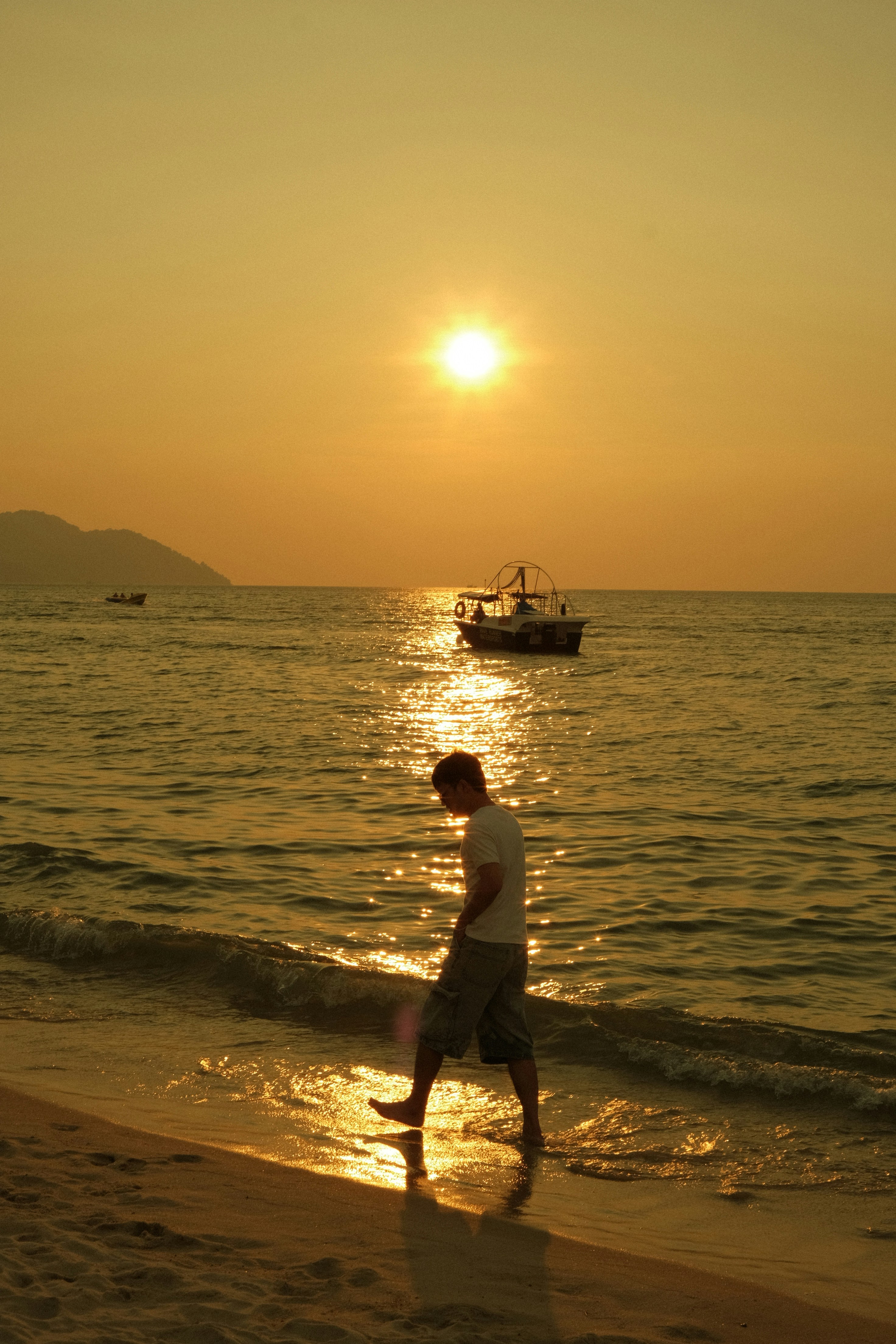 Sunlit Solitude: A lone walker along the shore at golden hour