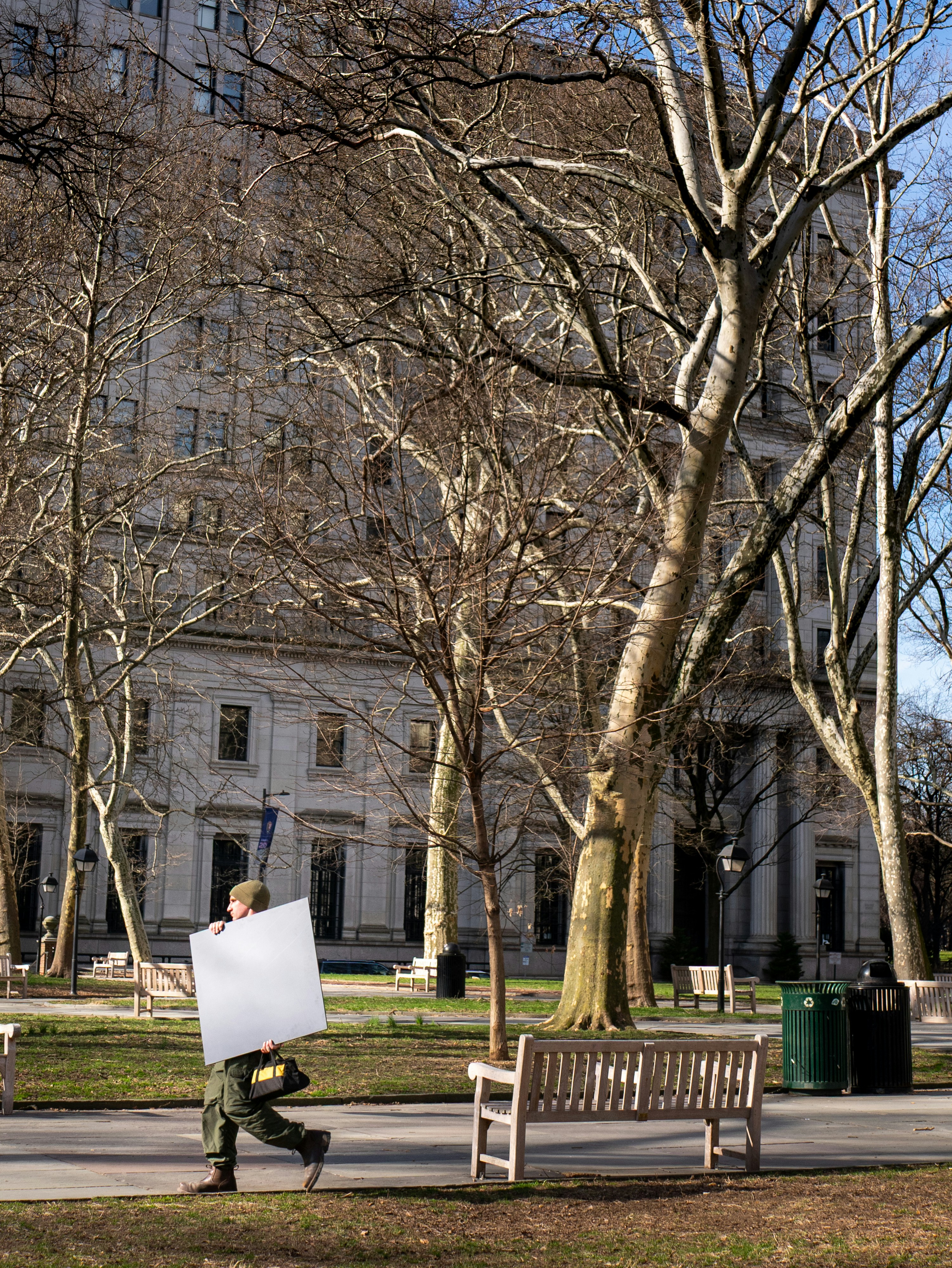 Man with Blank Banner Passes Between Park Benches in Urban Square