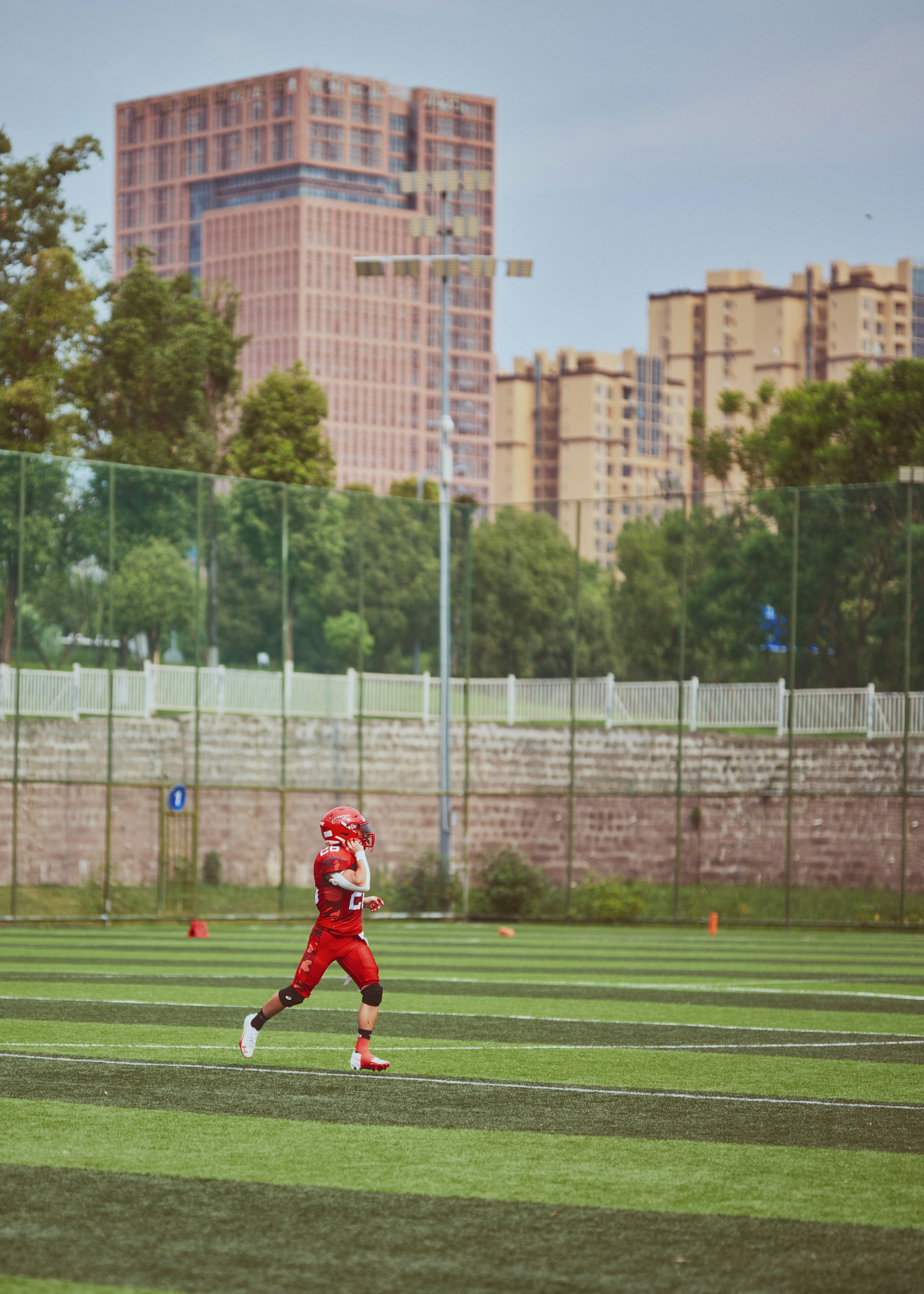 Red-jersey Runner on a Green Field under Urban Skyline