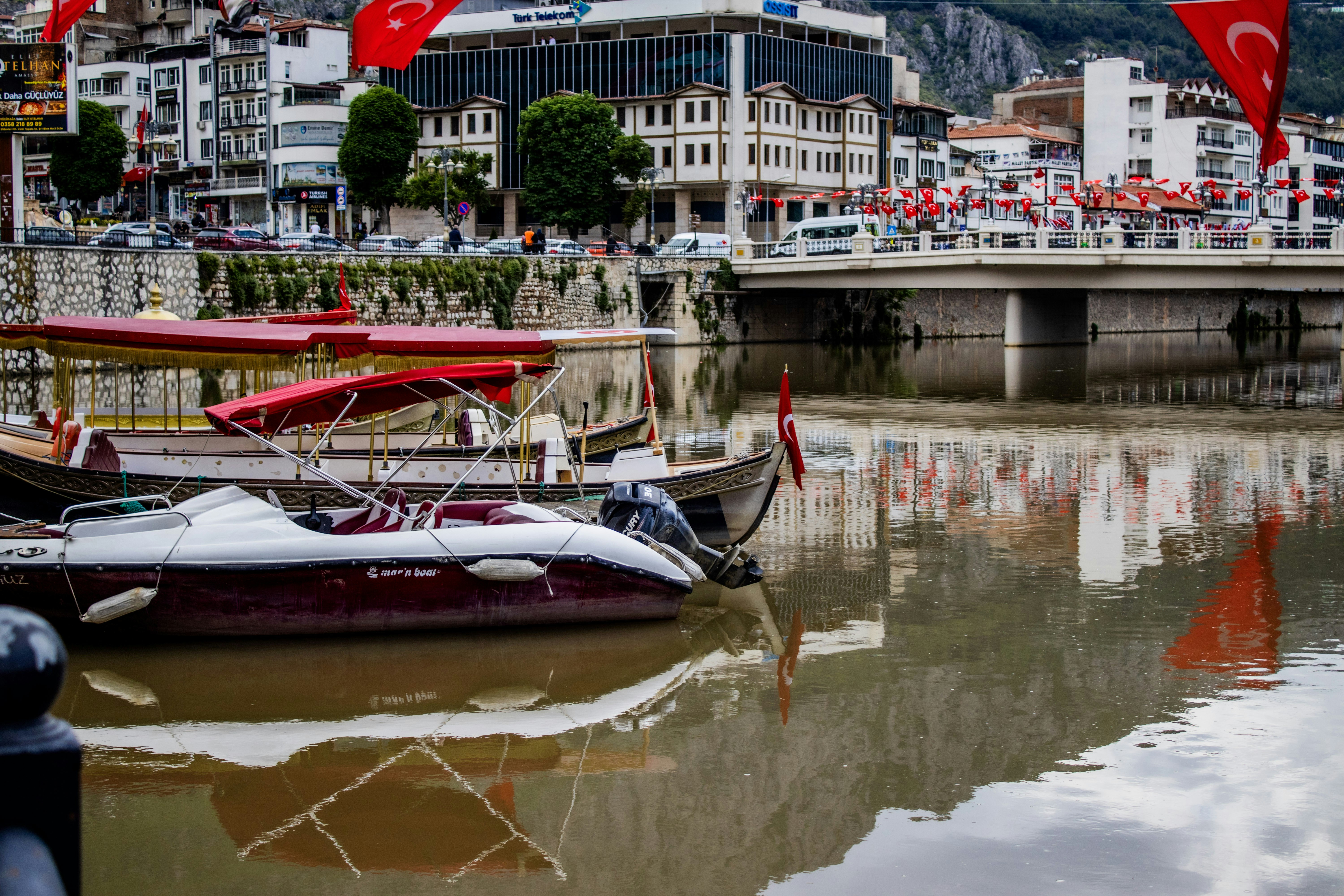 Turkish riverside: red flags, boats, and a wake of reflections