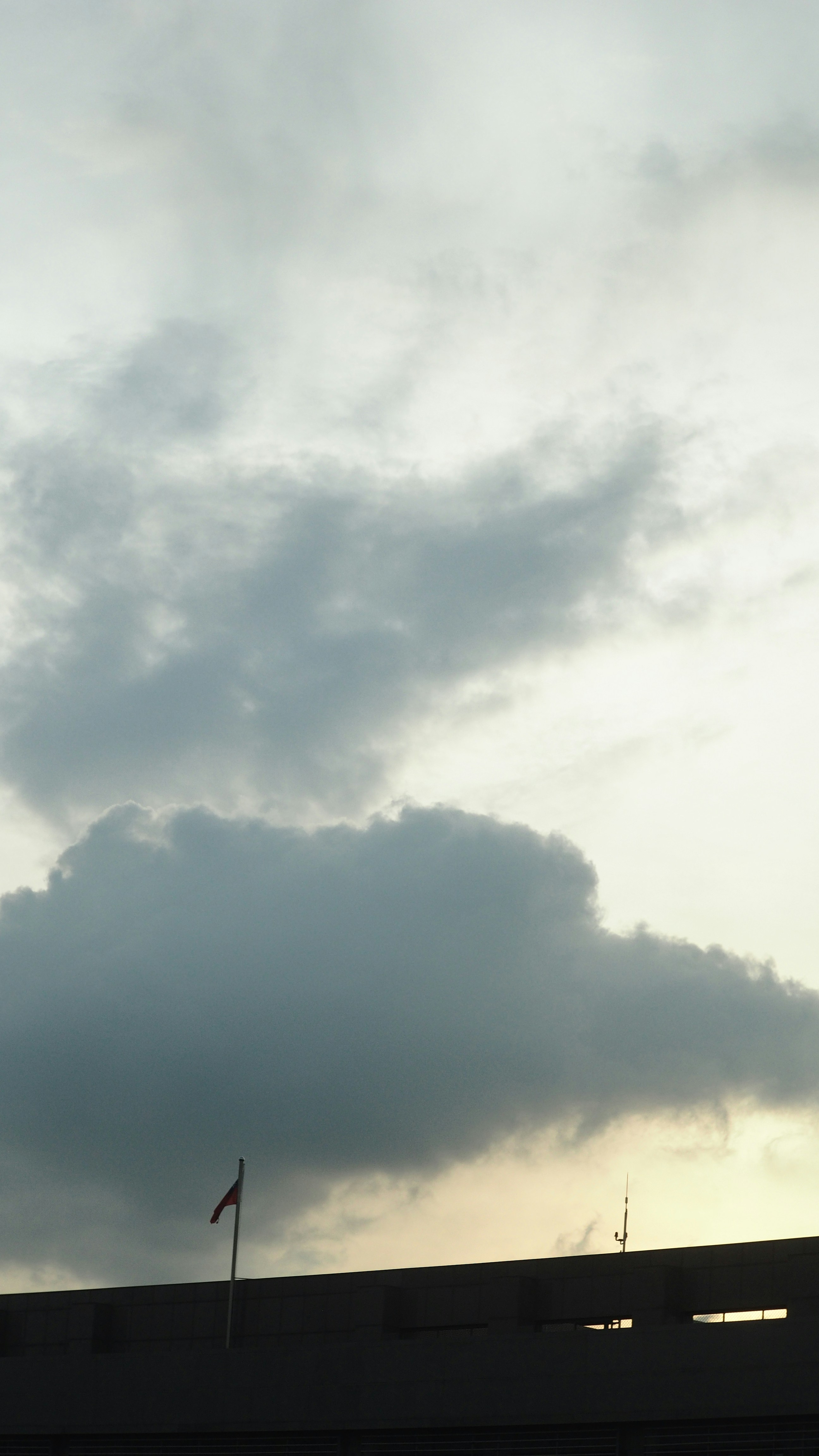 Edge of Daylight: Silhouetted Rooftop Flag beneath a Brooding Sky