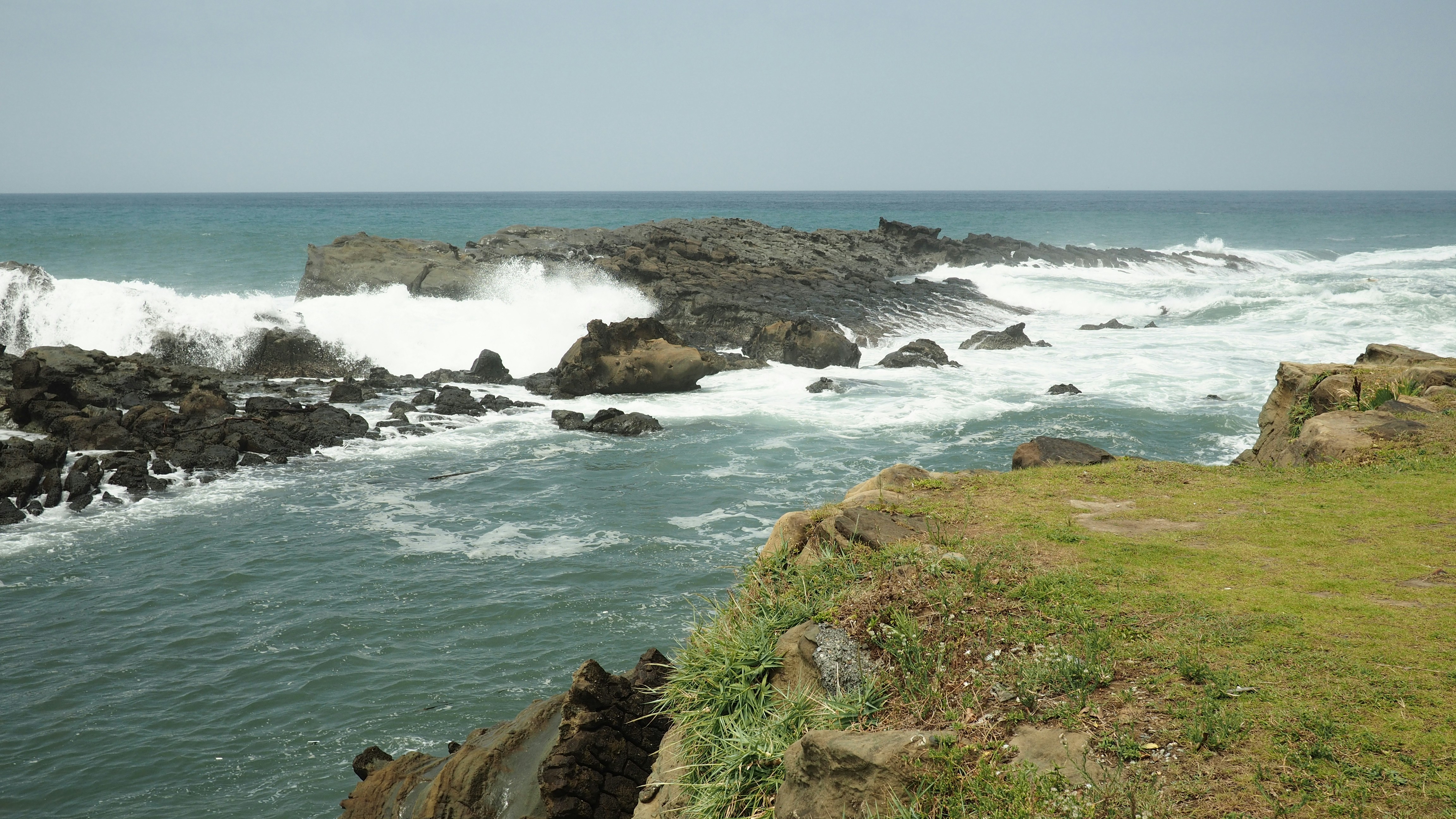 Coastal Edge: Waves Meet Weathered Grass and Rocks