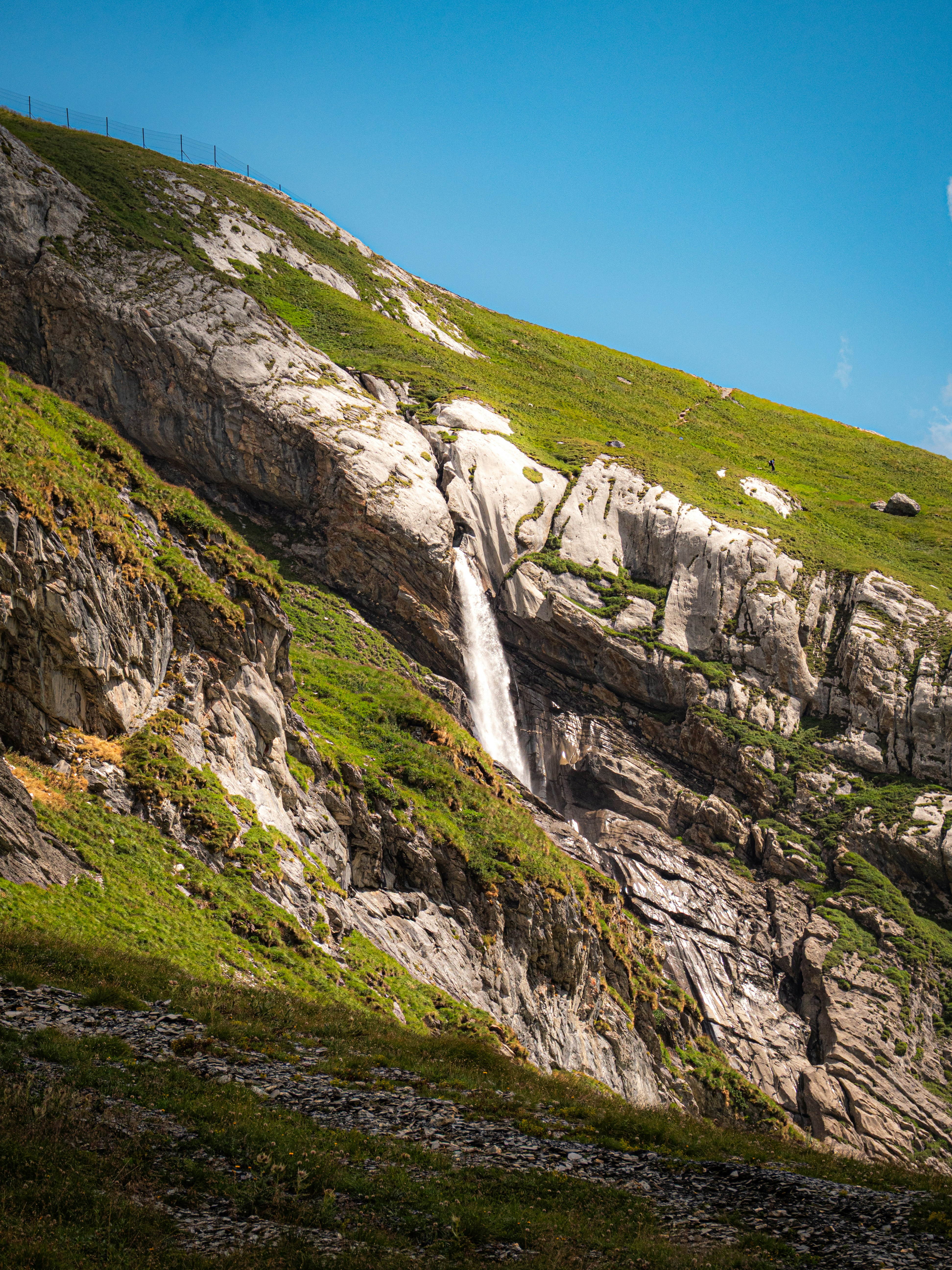 A Narrow Waterfall Stripes the Green Mountain Side