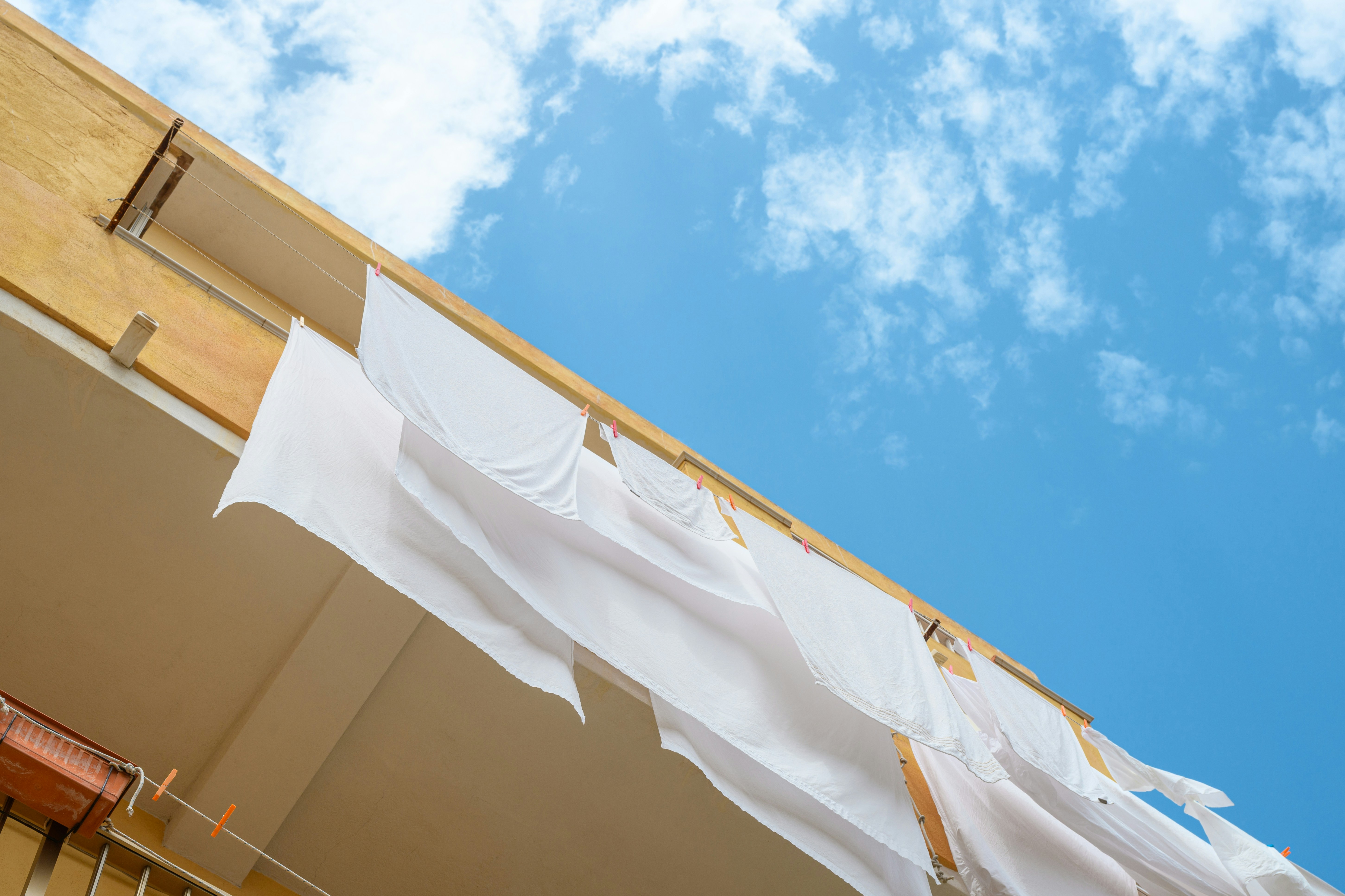White laundry billows against a bright blue sky from a sunlit balcony