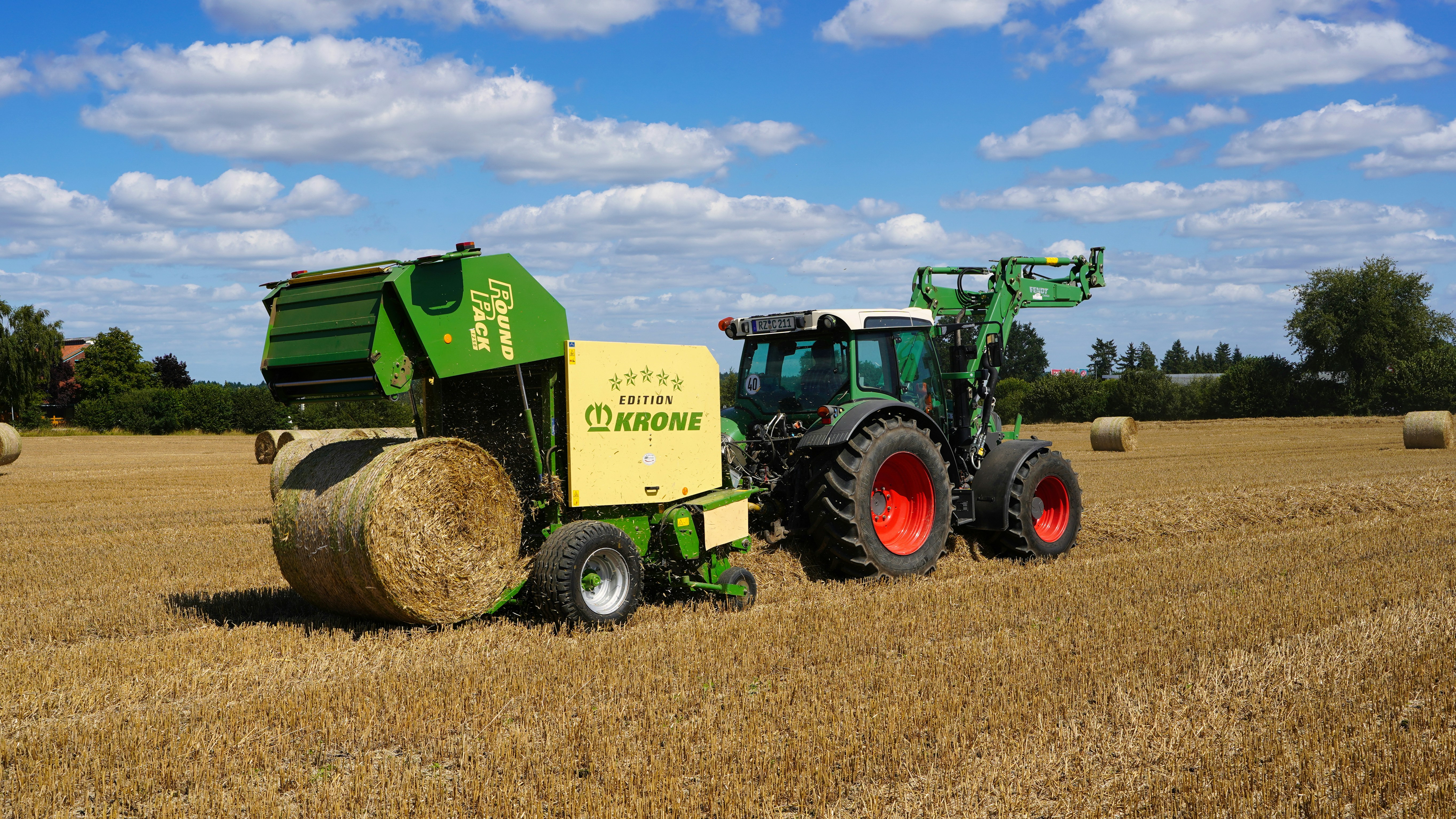 Harvest Machinery at Dusk: A Green Combine Tugs a Bales-and-Baler Duo Across a Golden Field