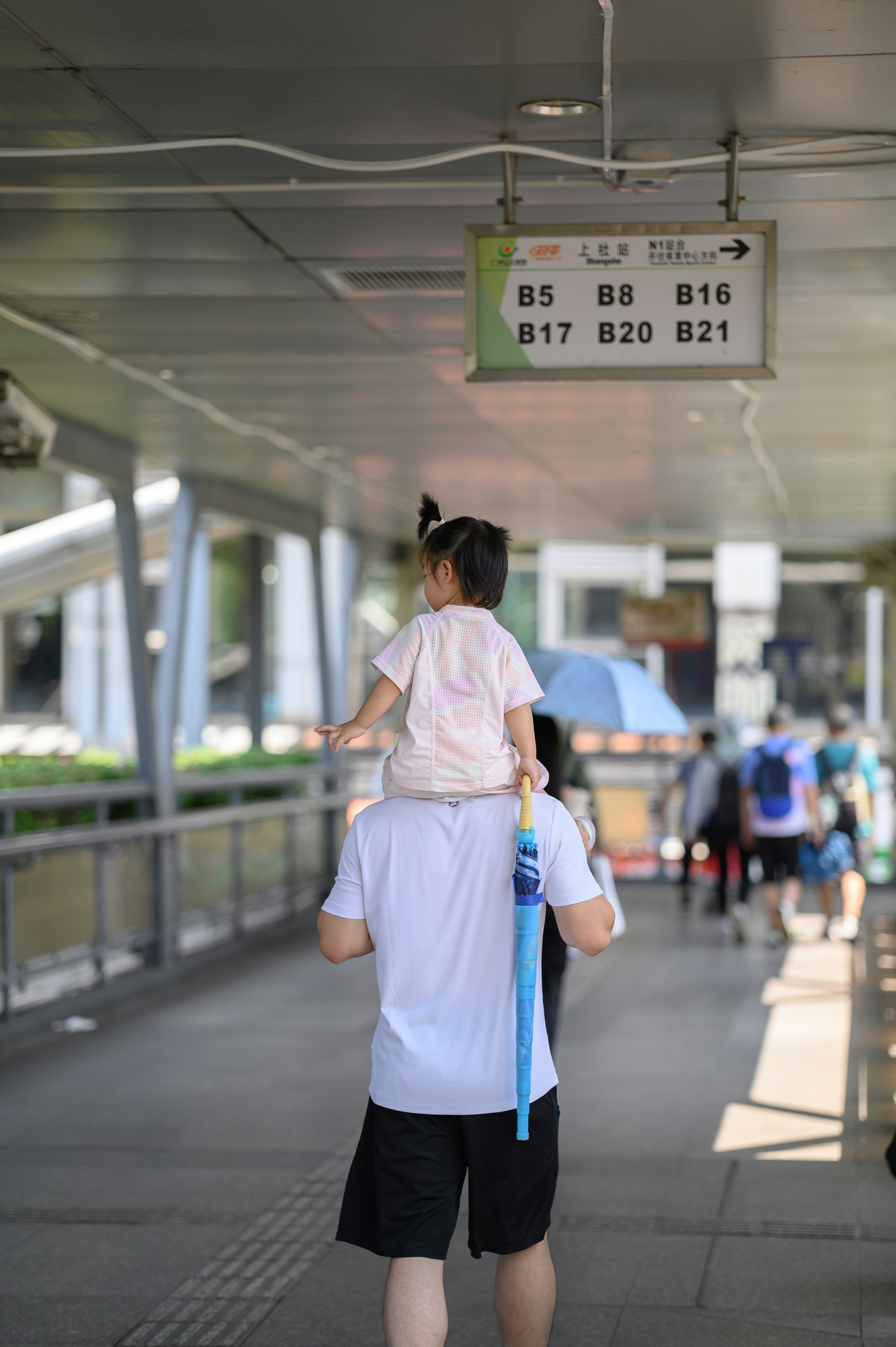 An adult carrying a child on their shoulders along a covered pedestrian walkway.