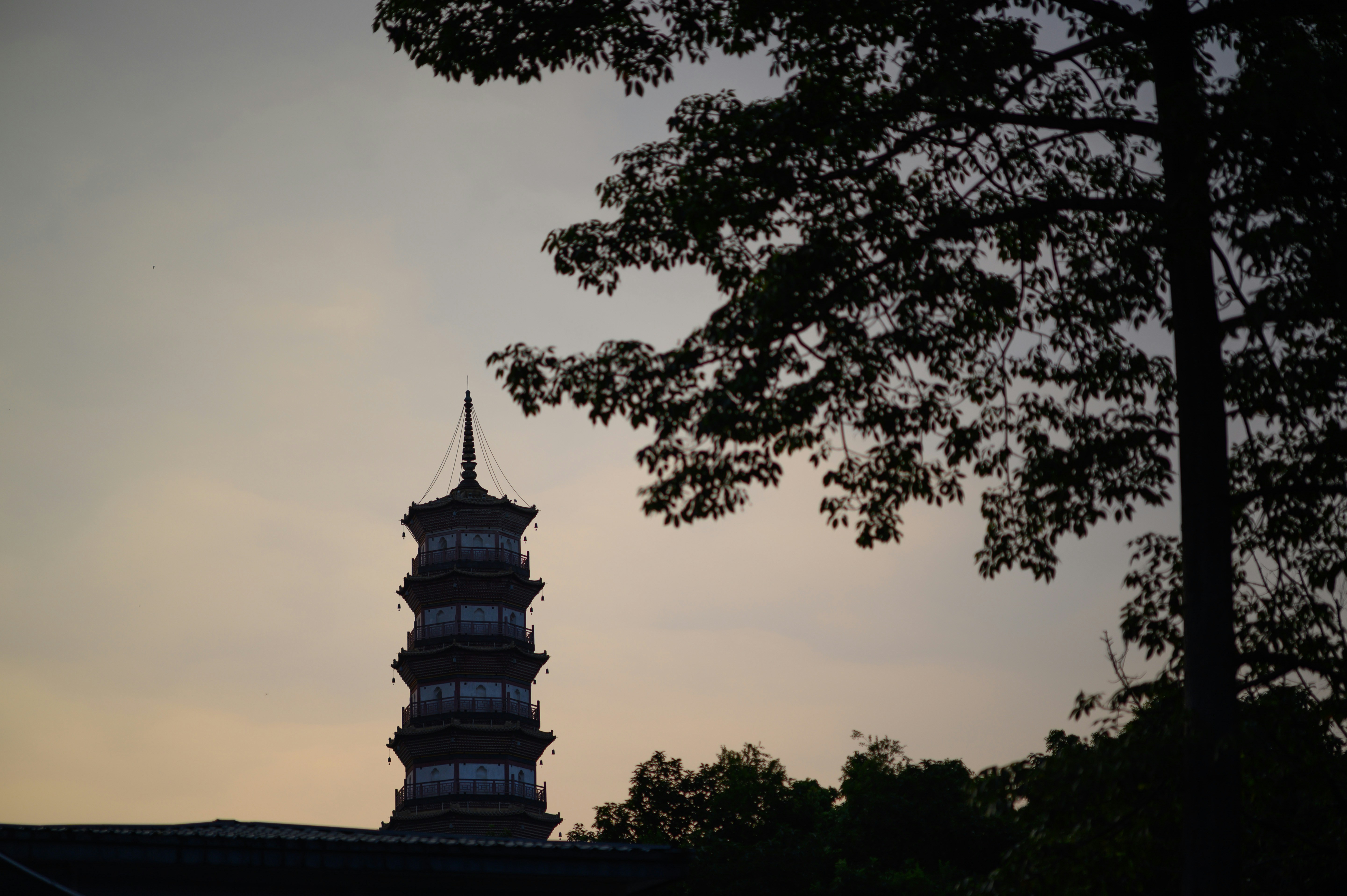Silhouette of a tiered pagoda under a shadowed canopy at golden hour