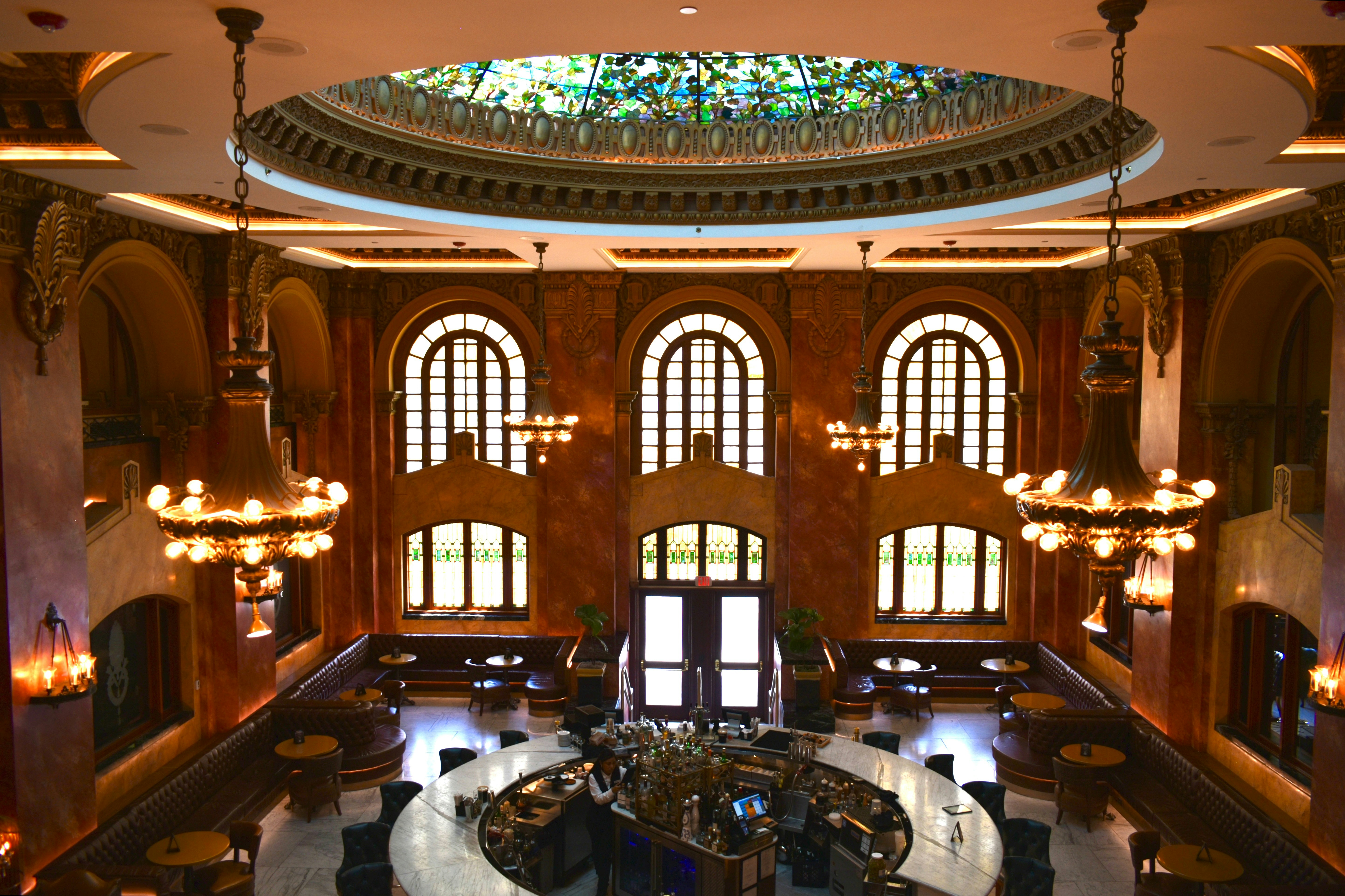 Grand, dusk-lit interior of a historic rotunda featuring a circular bar, arched windows, and ornate chandeliers.