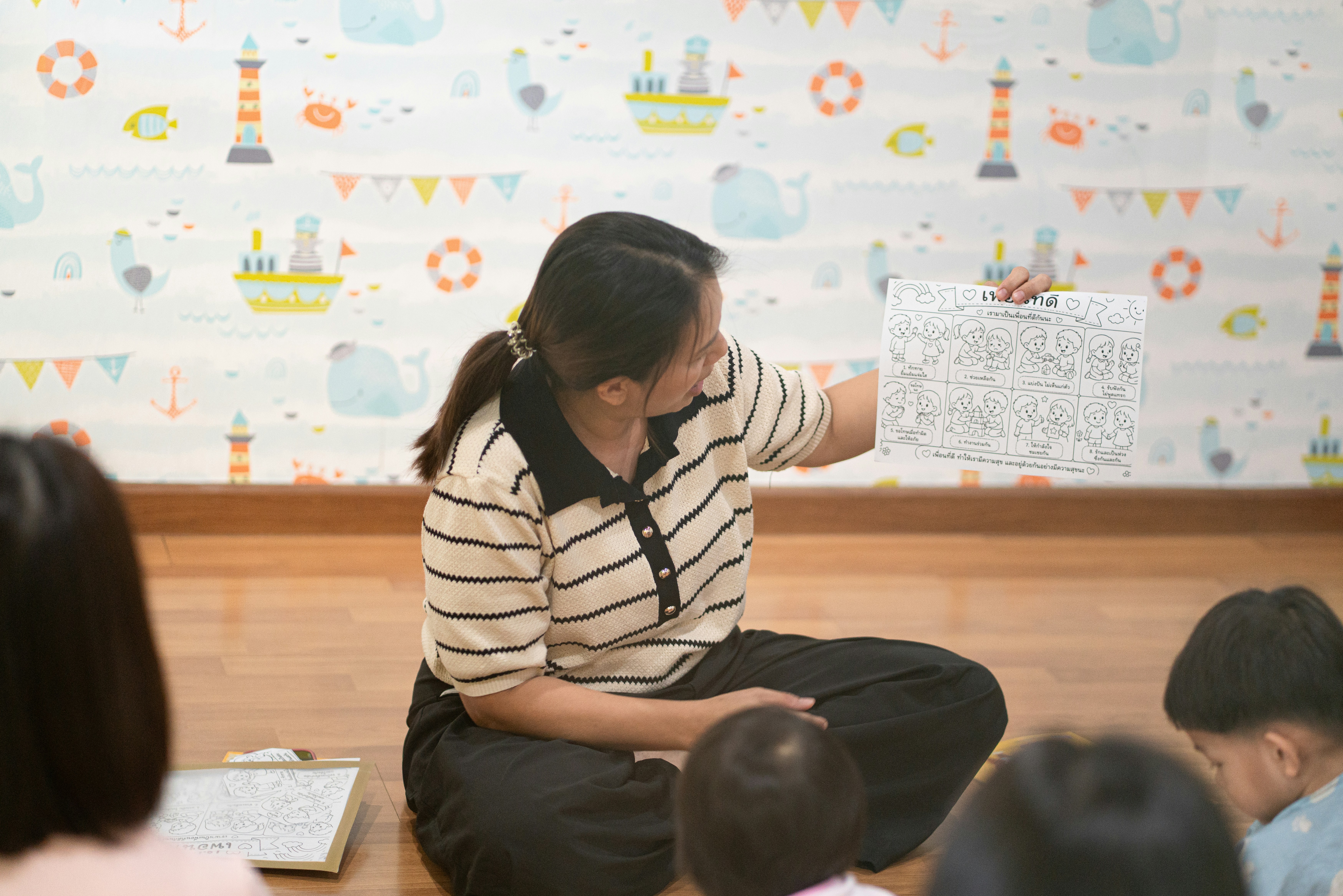 Educator reading a printed page to children during a classroom circle time in a bright, colorful room.