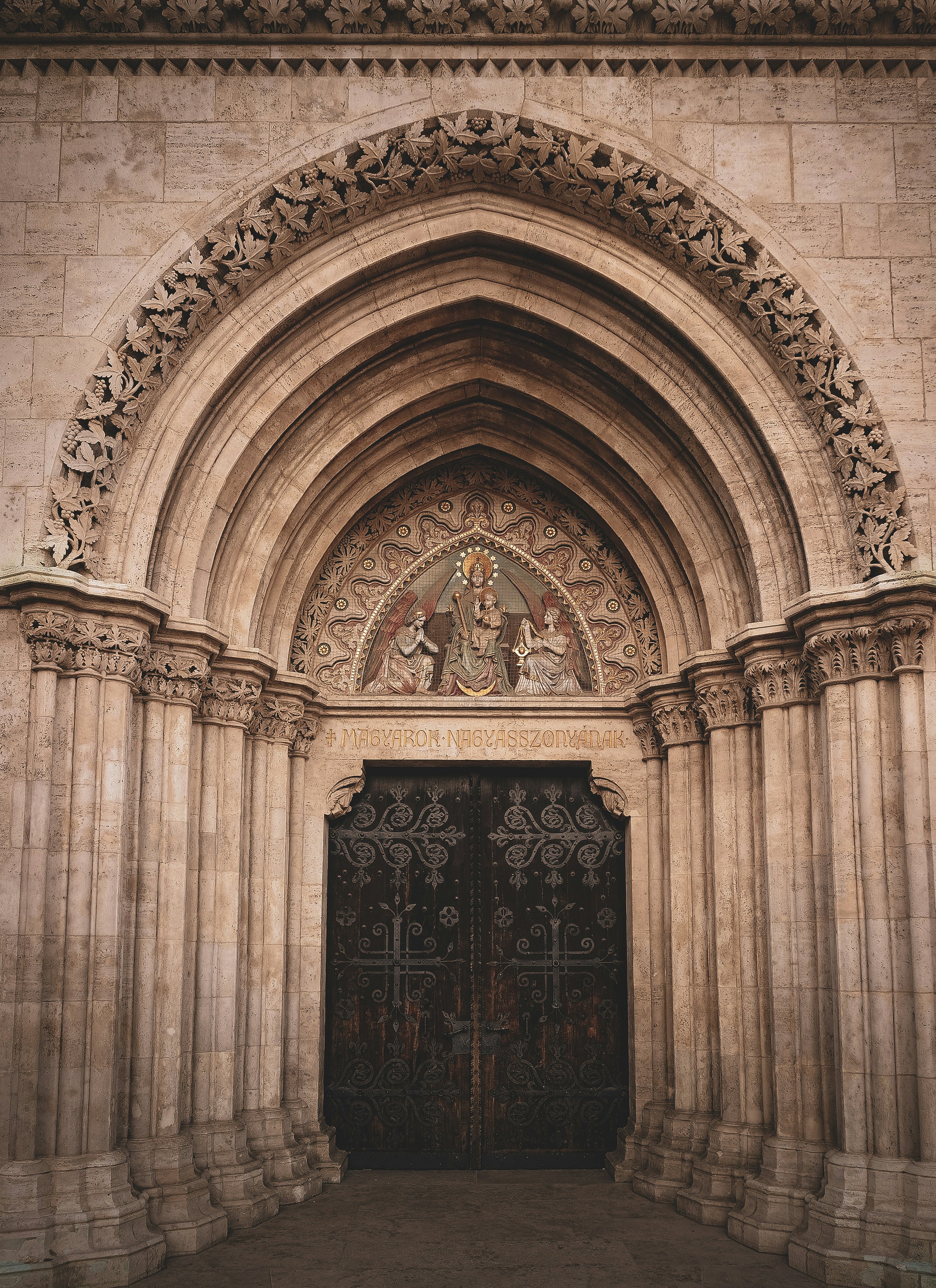 Ancient stone archway with ornate doorway and detailed carvings, forming a grand entrance framed by columns and sculpted reliefs.