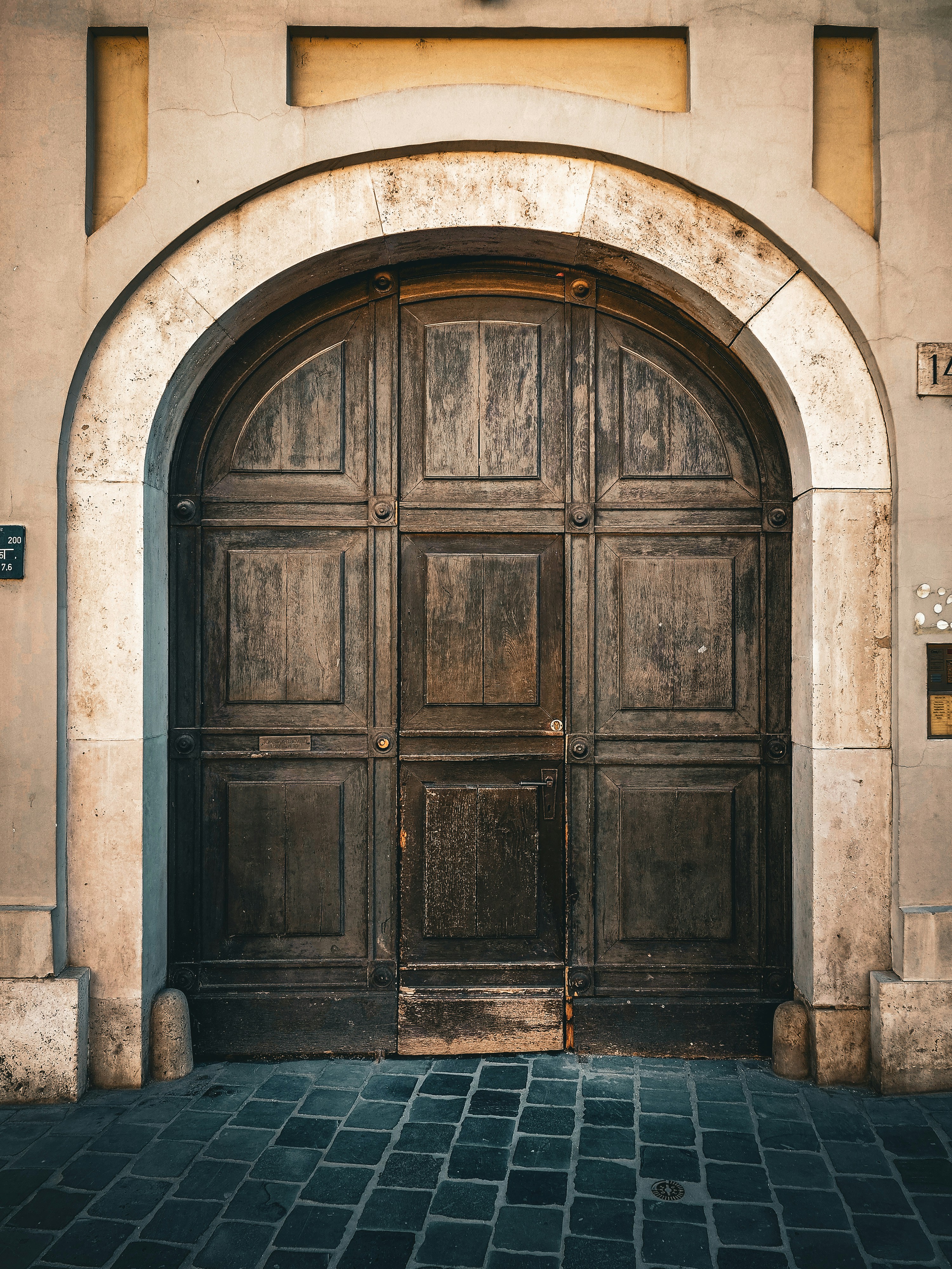Rustic wooden door set within a weathered stone arch, anchored by a cobblestone doorstep and worn metal fixtures.