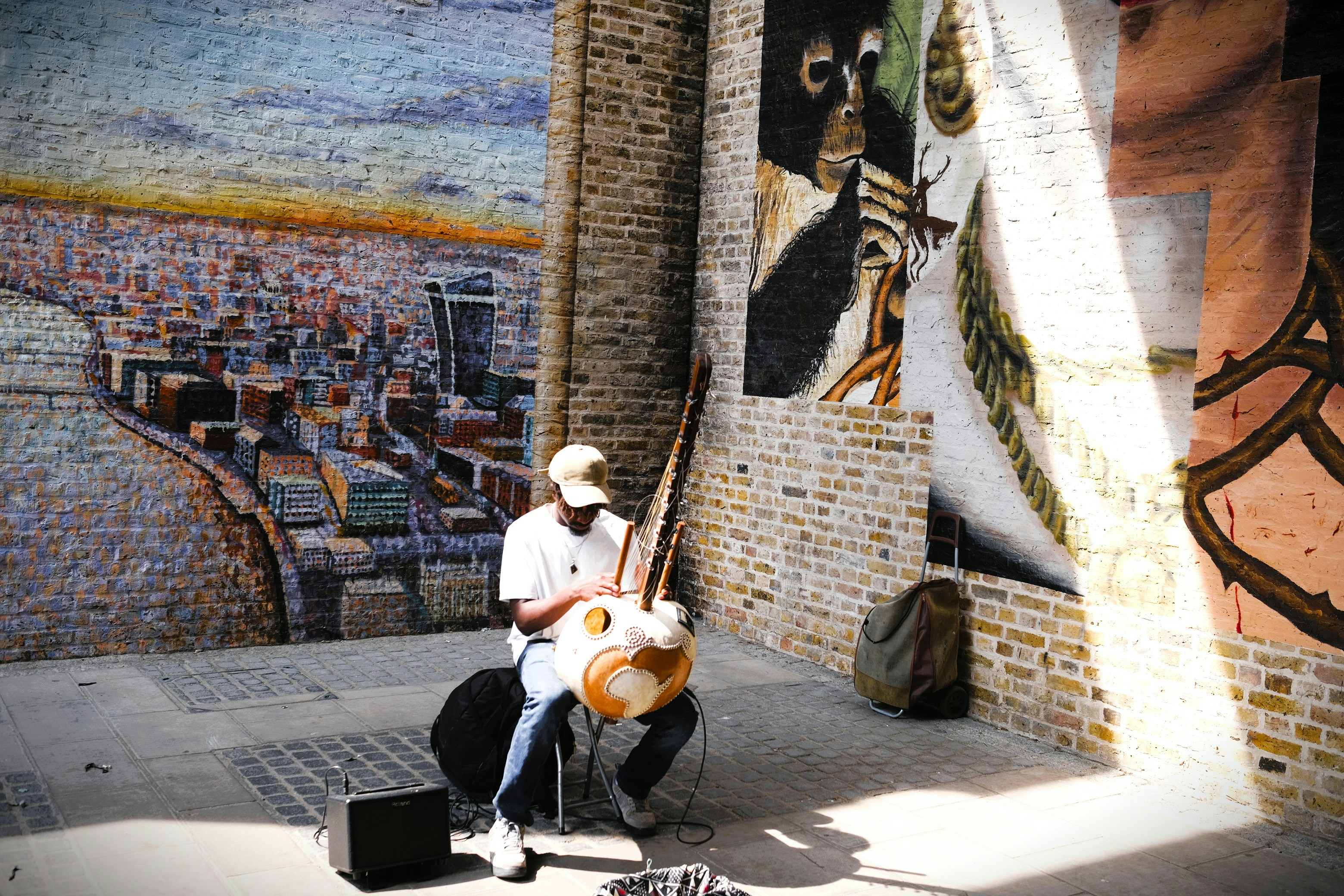 Street musician at the sunlit brick mural, framed by colorful walls