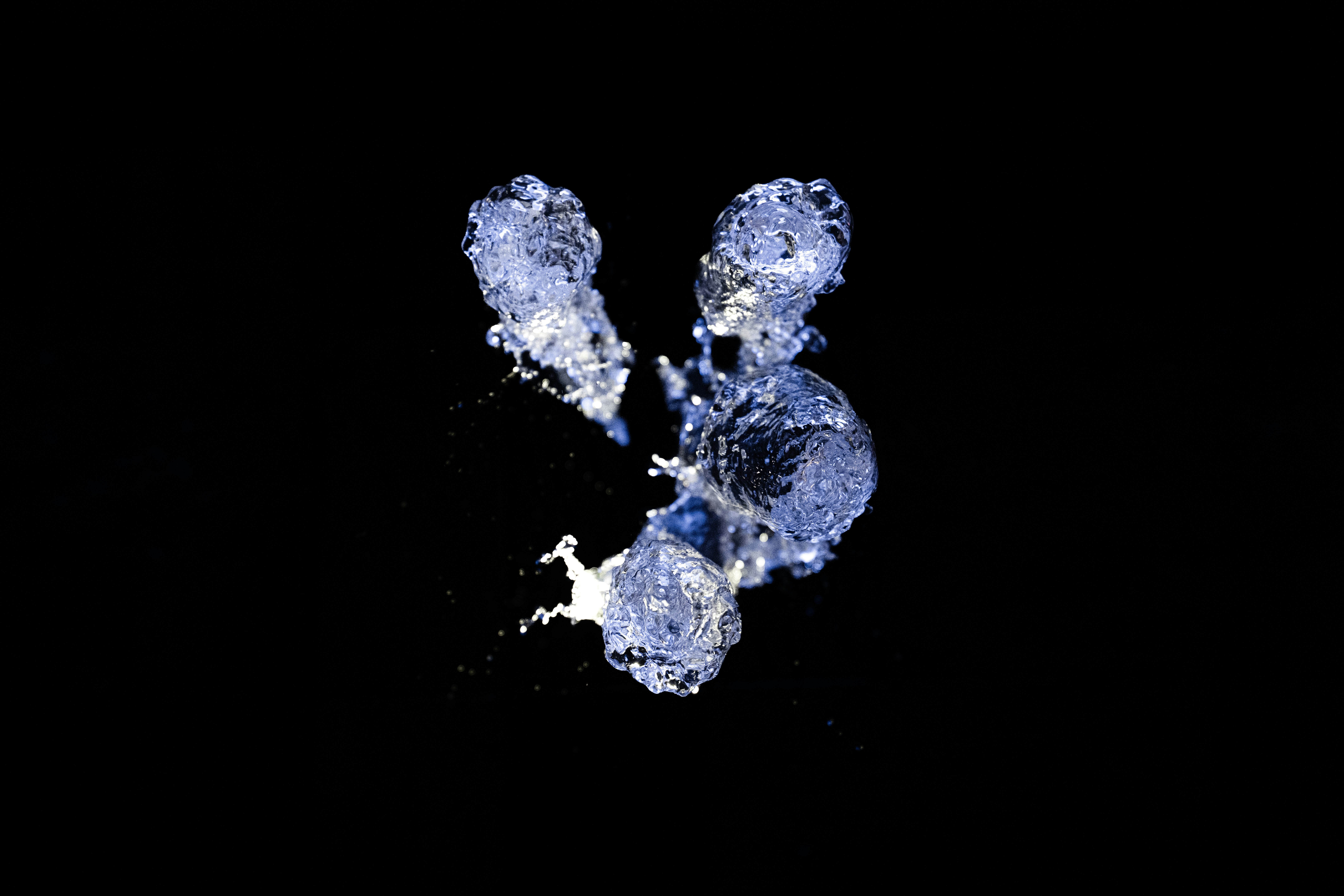 Three fused blue ice fragments suspended against a black background, highlighting texture and translucence with a stark minimalist composition.