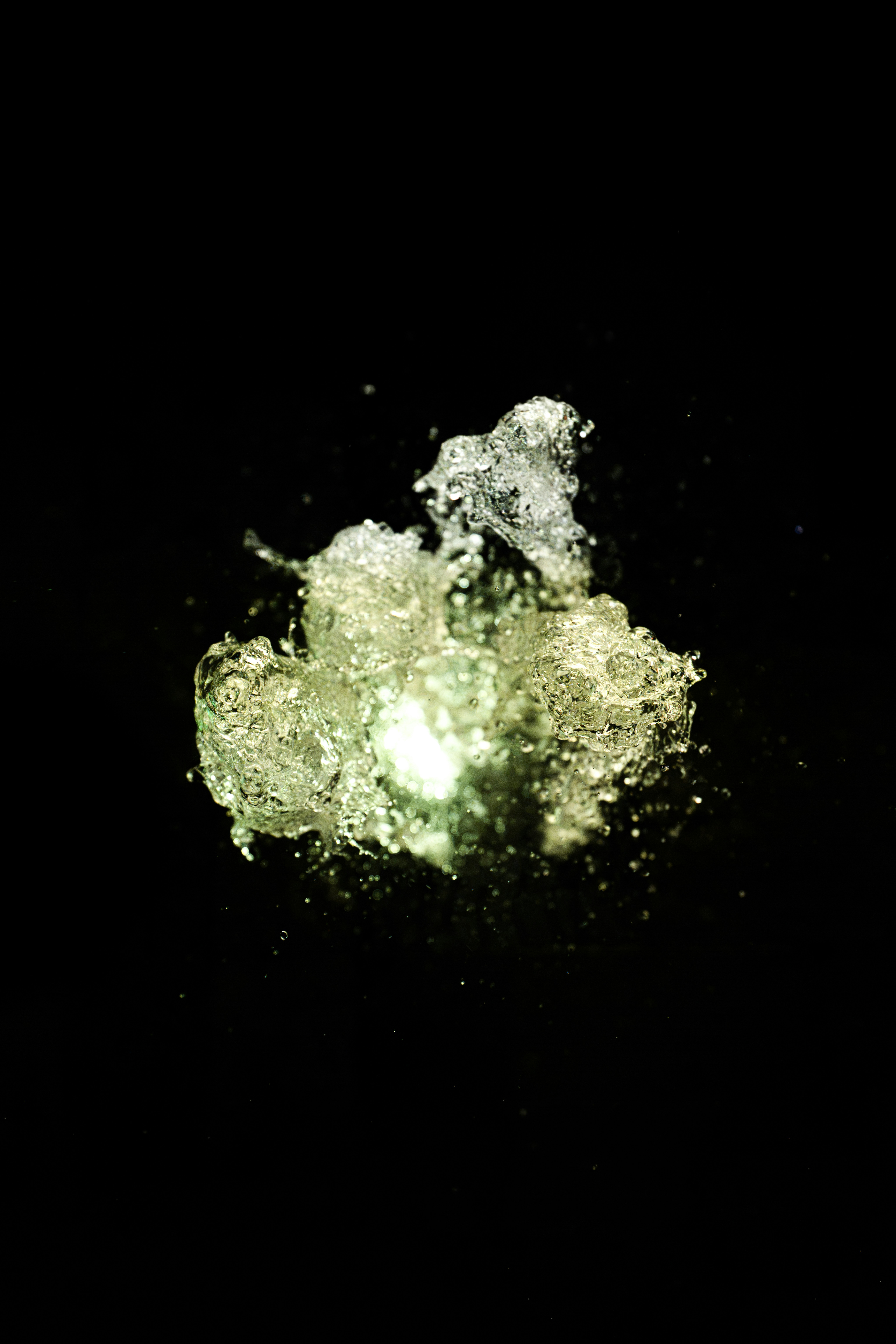 Liquid Burst in Darkness: Emerald Glow from a Floating Fragment