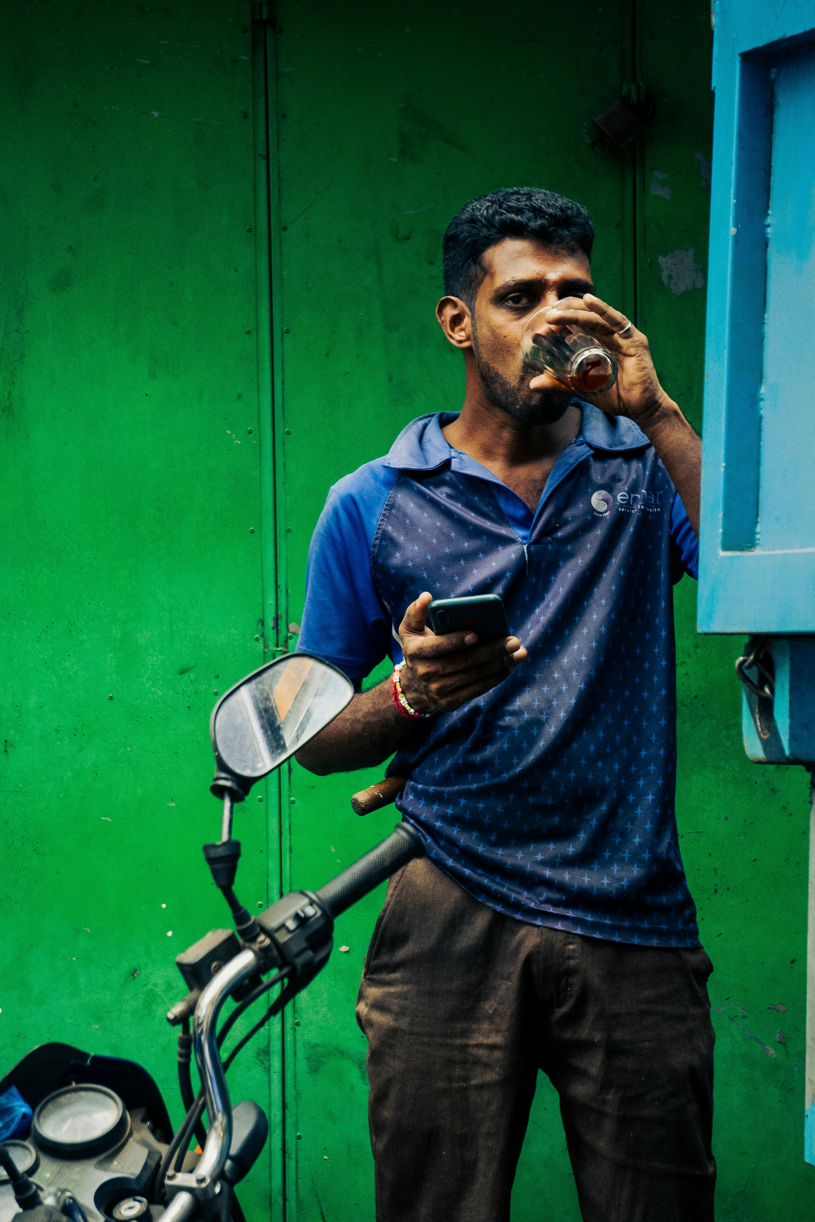 Midday Moments: A man on a green curb sipping and swiping with a motorcycle at his side