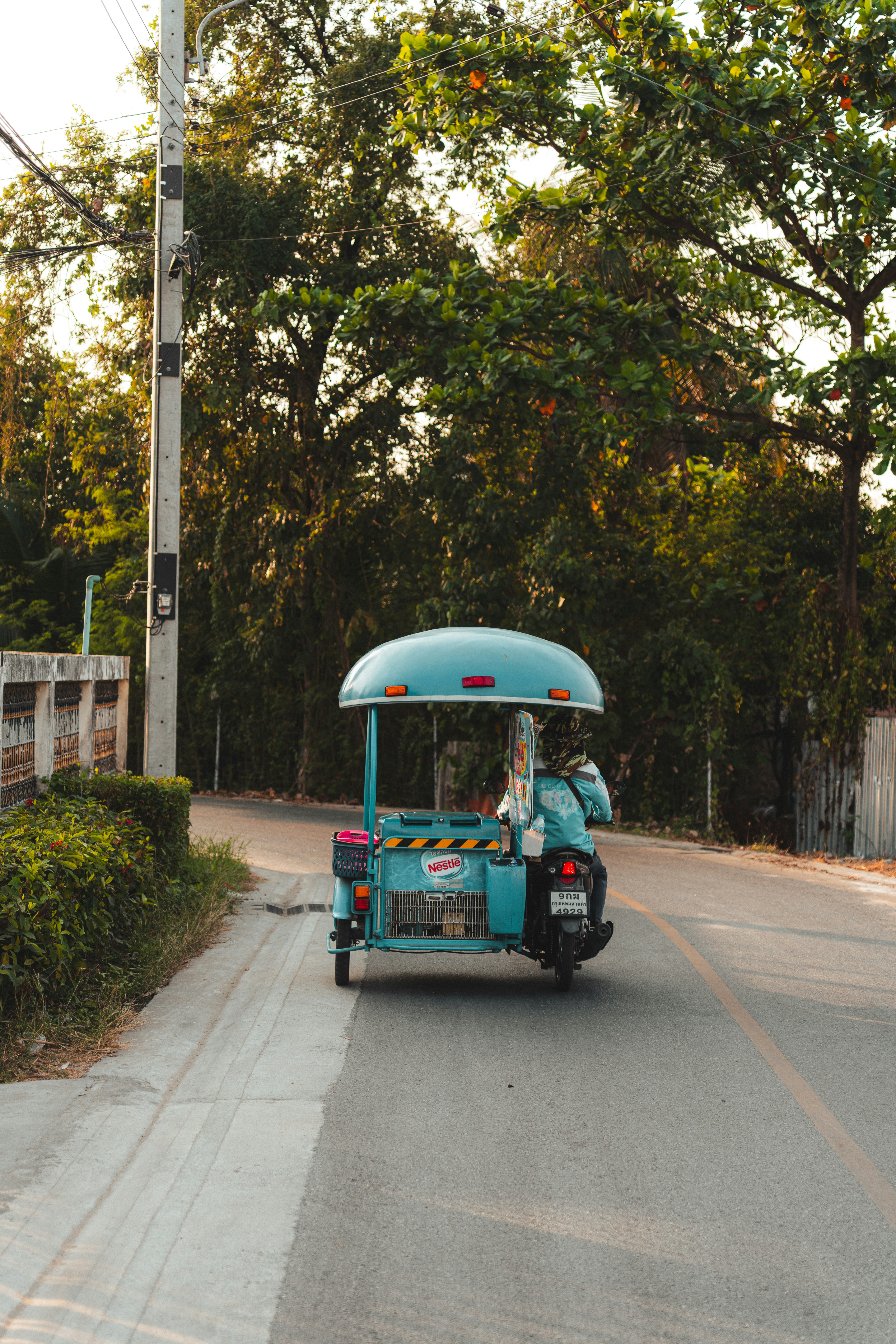 Blue rickshaw on a sunlit street: a quiet ride toward the trees