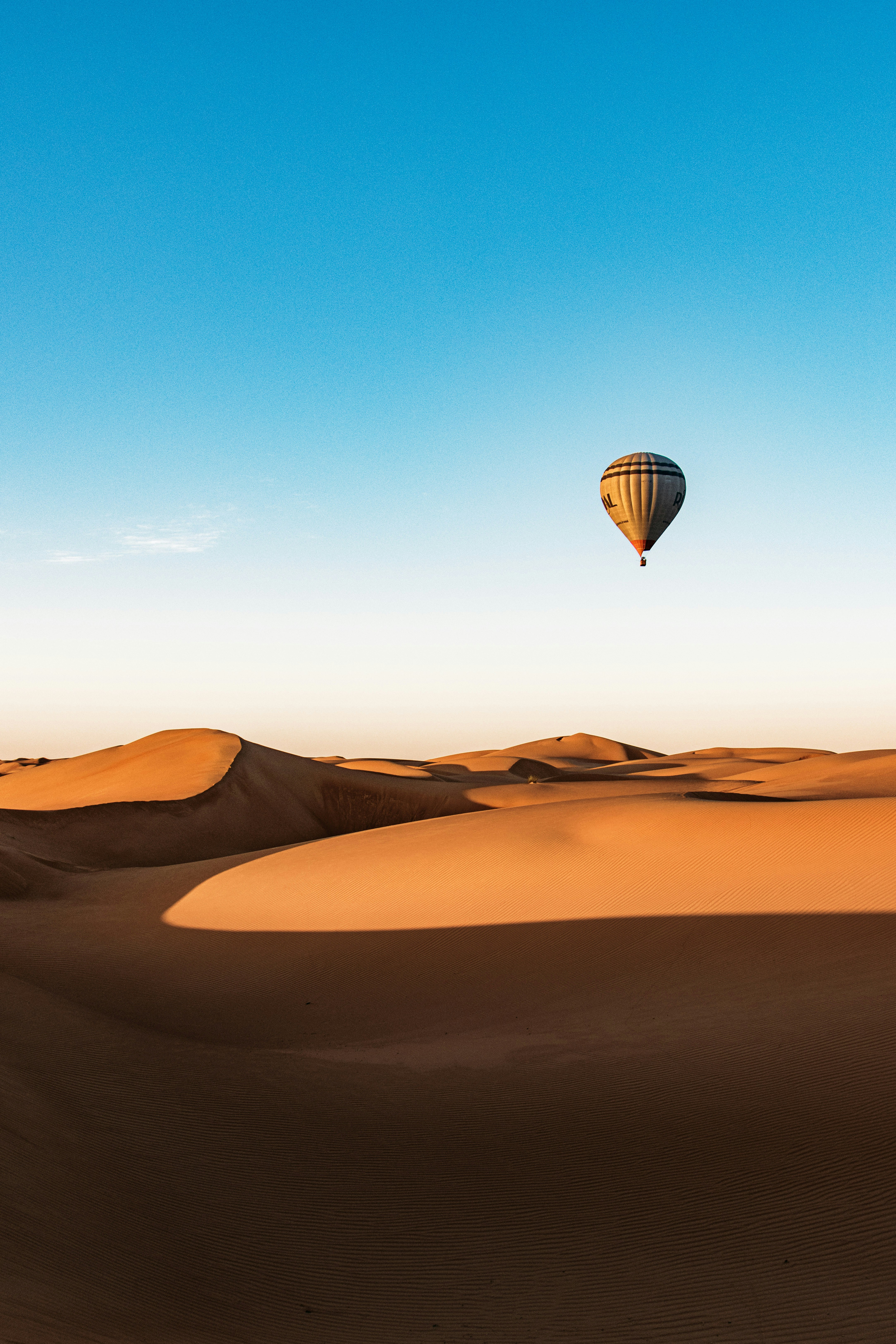 Desert High: A lone hot-air balloon drifts above sunlit dunes at dusk