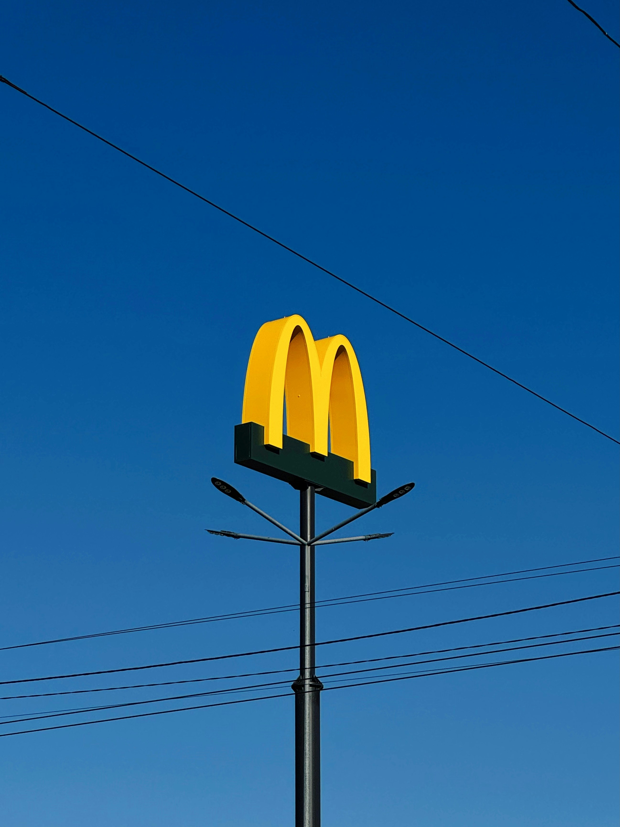 A yellow McDonald's golden arches sign on a pole against a clear blue sky