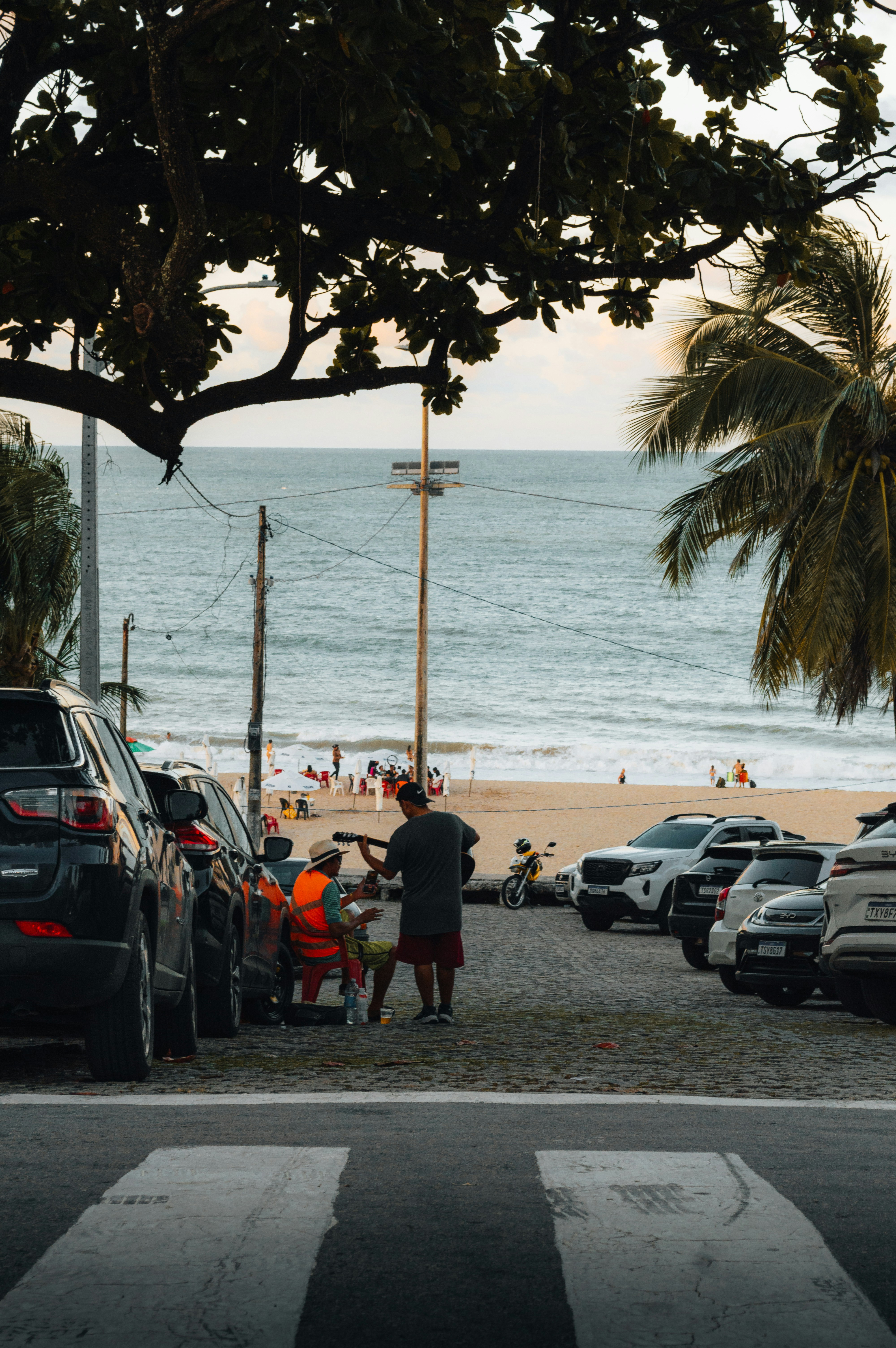 Beachfront Pause: A Couple and a Crew of Cars Framed by Tropical Shade