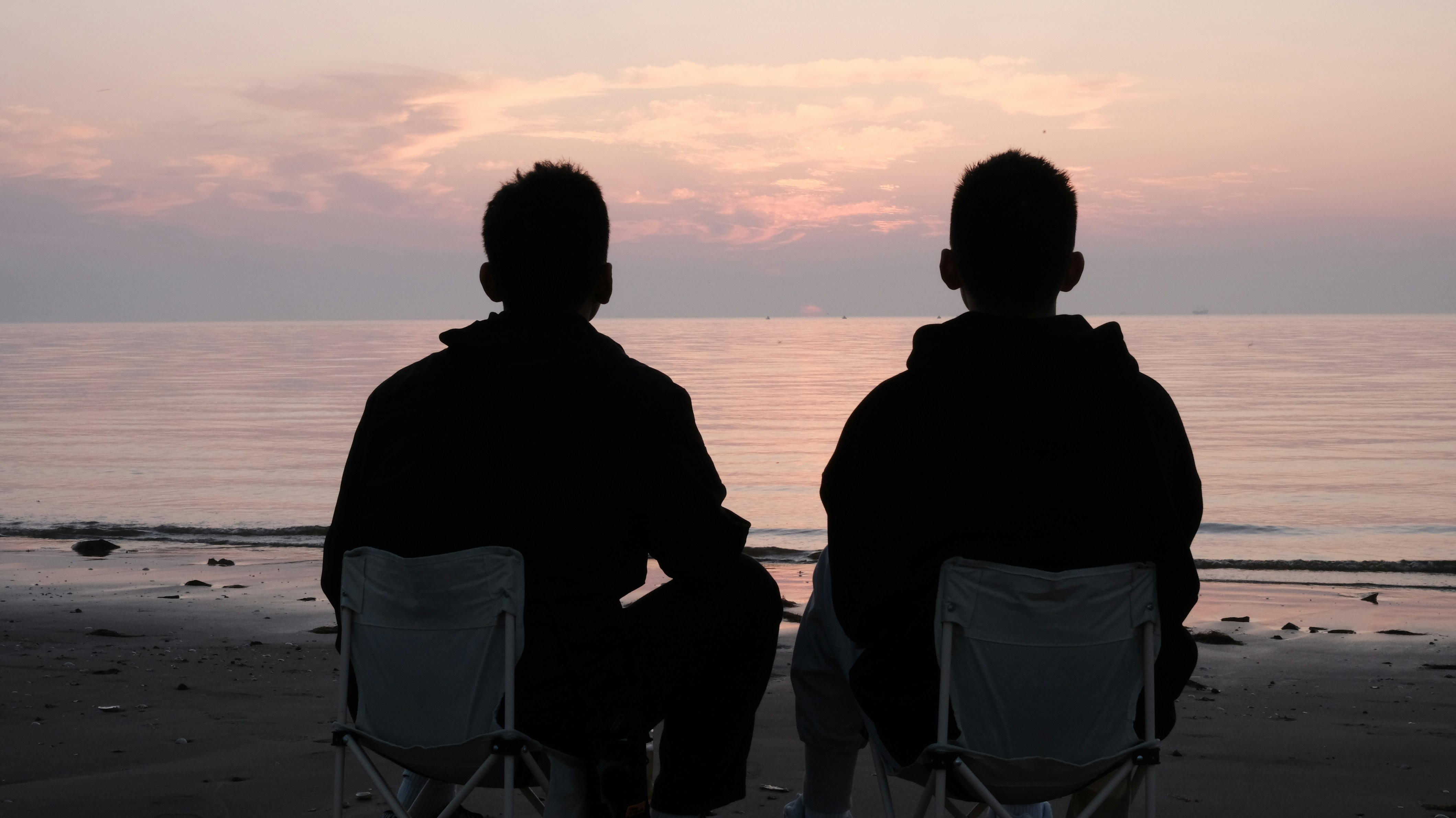 Twin Silhouettes at Dusk: Two Figures Meeting the Sea