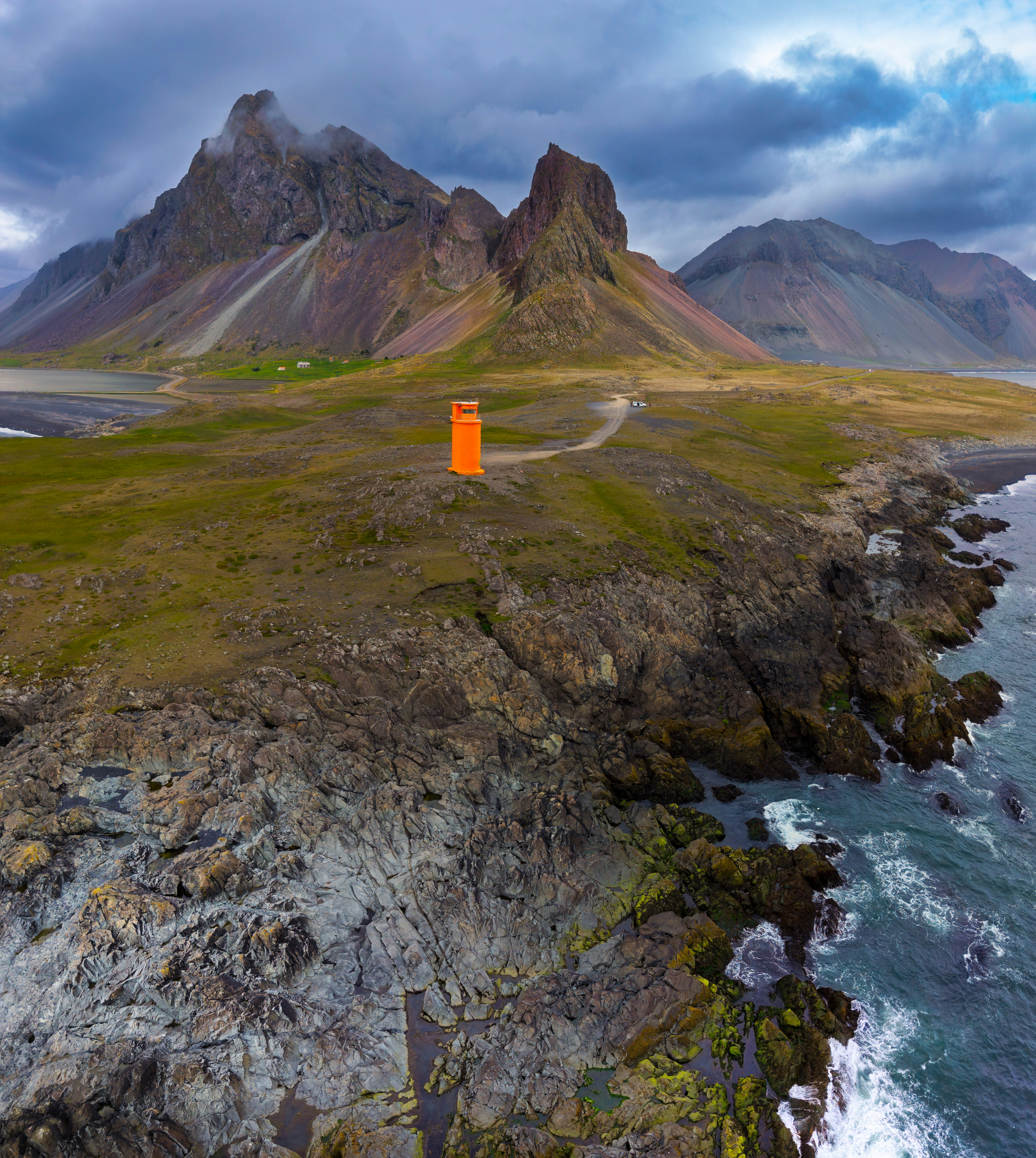 Orange beacon on windswept cliff beneath jagged volcanic peaks