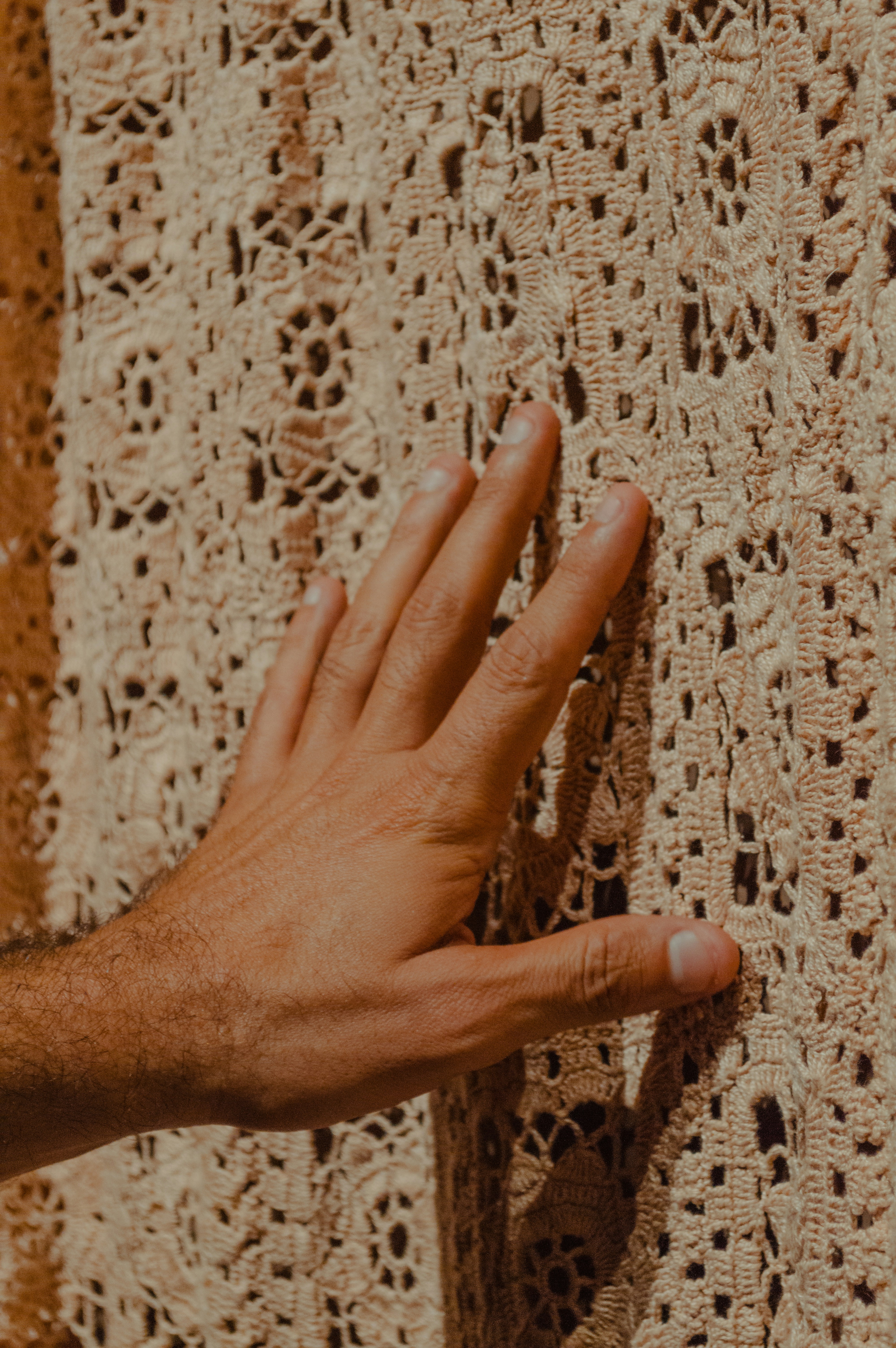 Hand Gently Tracing Lace: Texture and Warmth in Sunlit Crochet