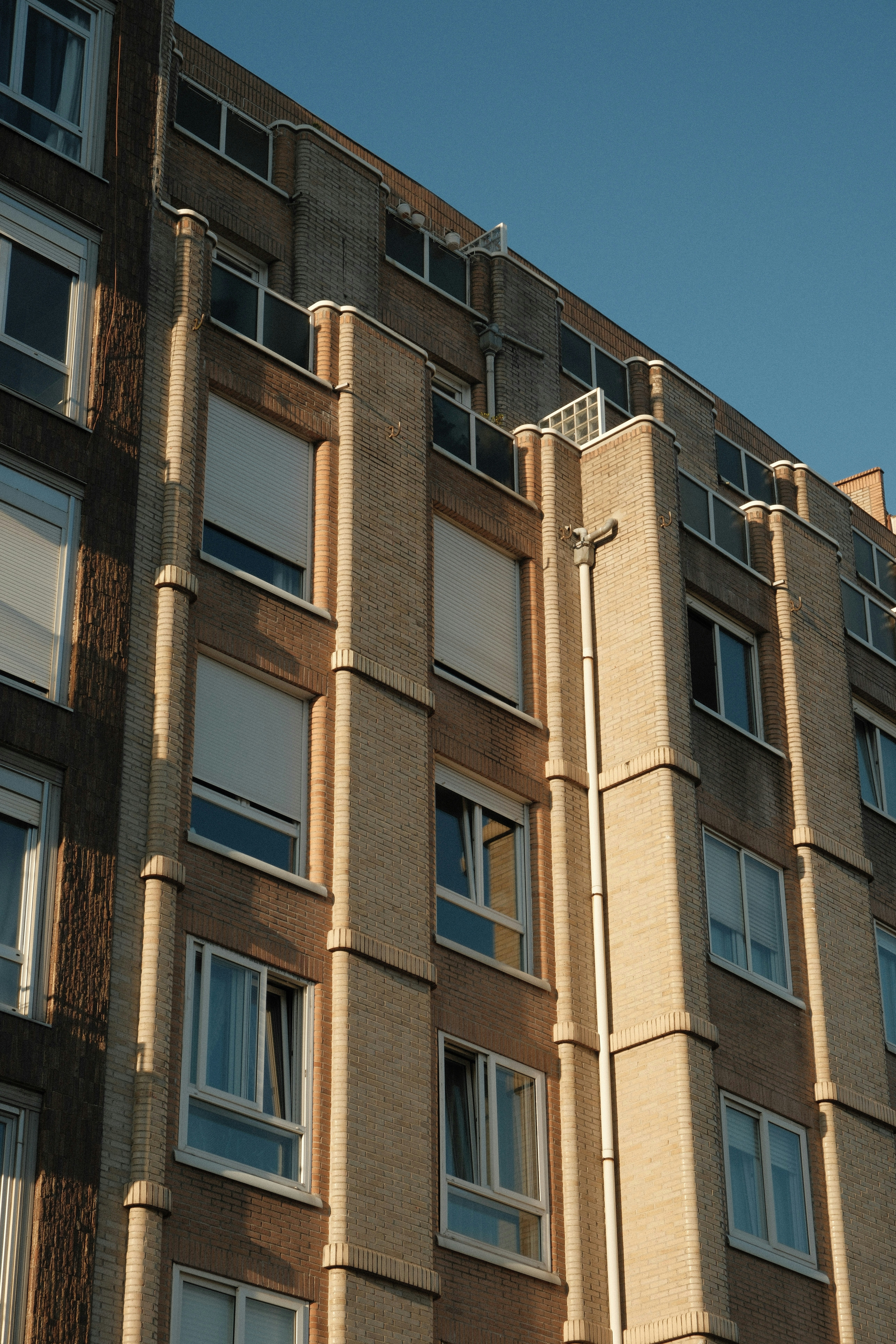 A brick apartment building facade with white window shutters under a clear blue sky